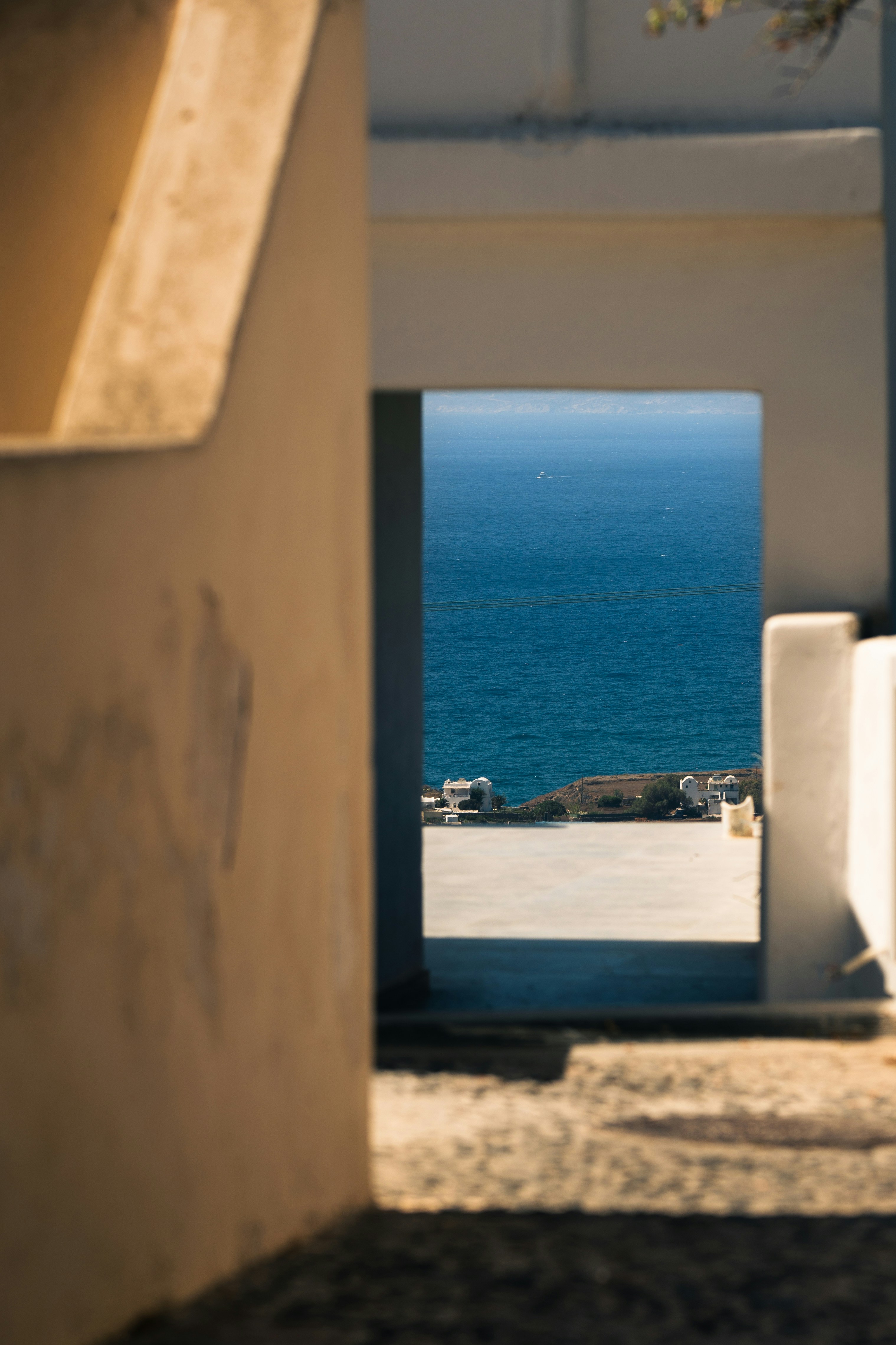 A narrow passageway reveals a stunning view of the deep blue sea, framed by rustic walls. The scene invites contemplation and tranquility.