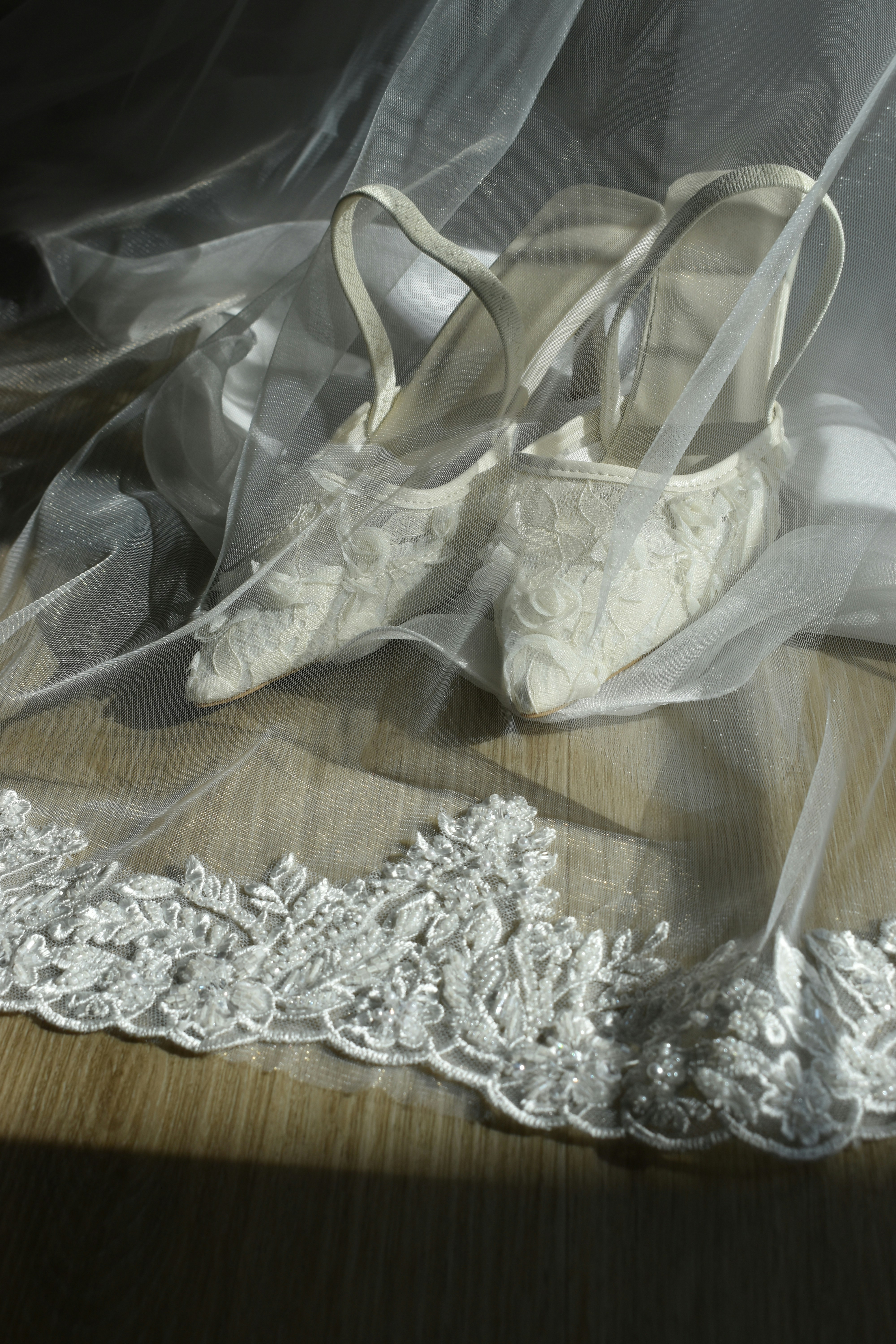Delicate lace wedding shoes resting on a soft veil, accompanied by intricate lace detailing. The composition highlights the charm of bridal accessories.
