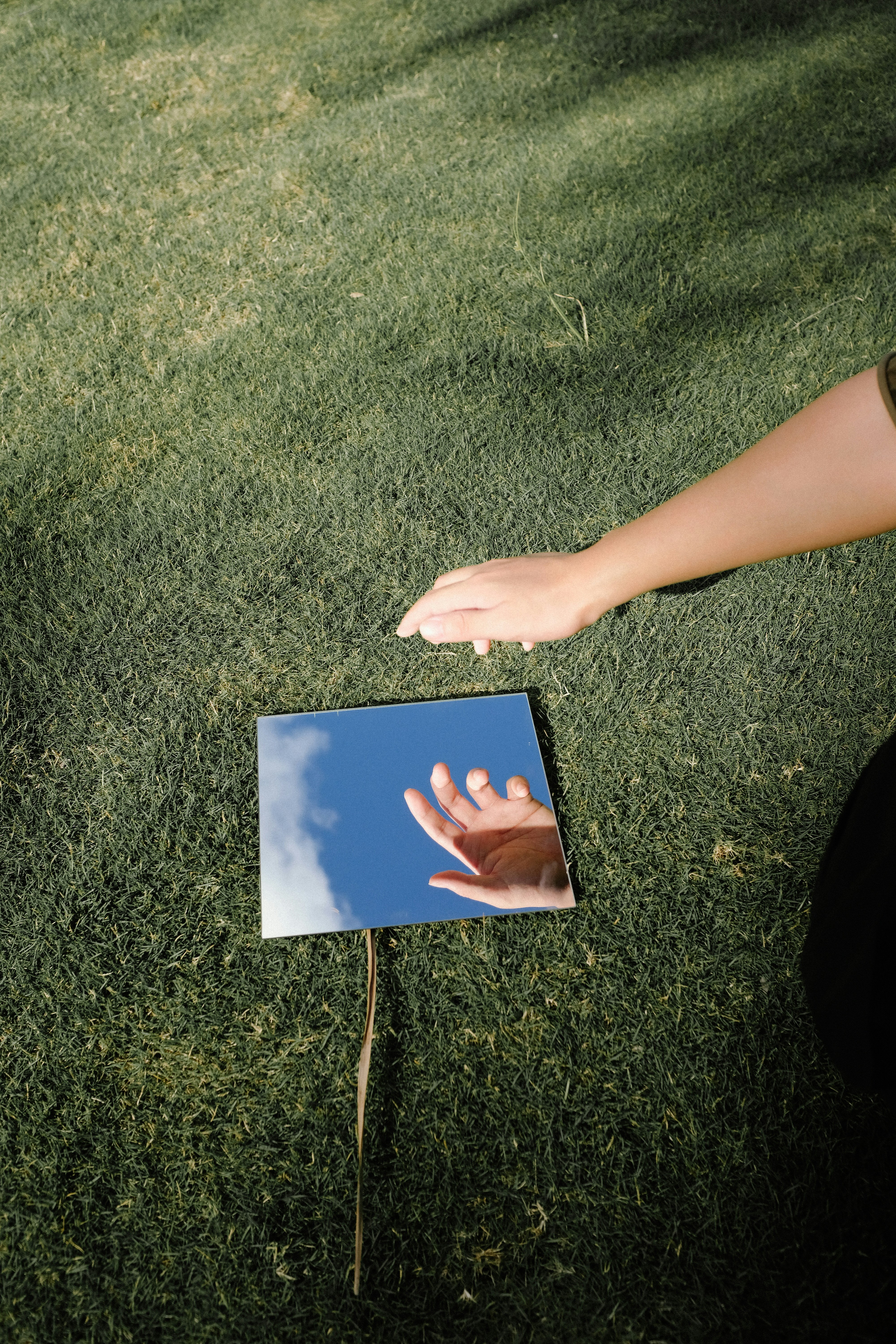 Lawn Mirror: Hand Reaches Toward the Sky Reflected in a Small Square