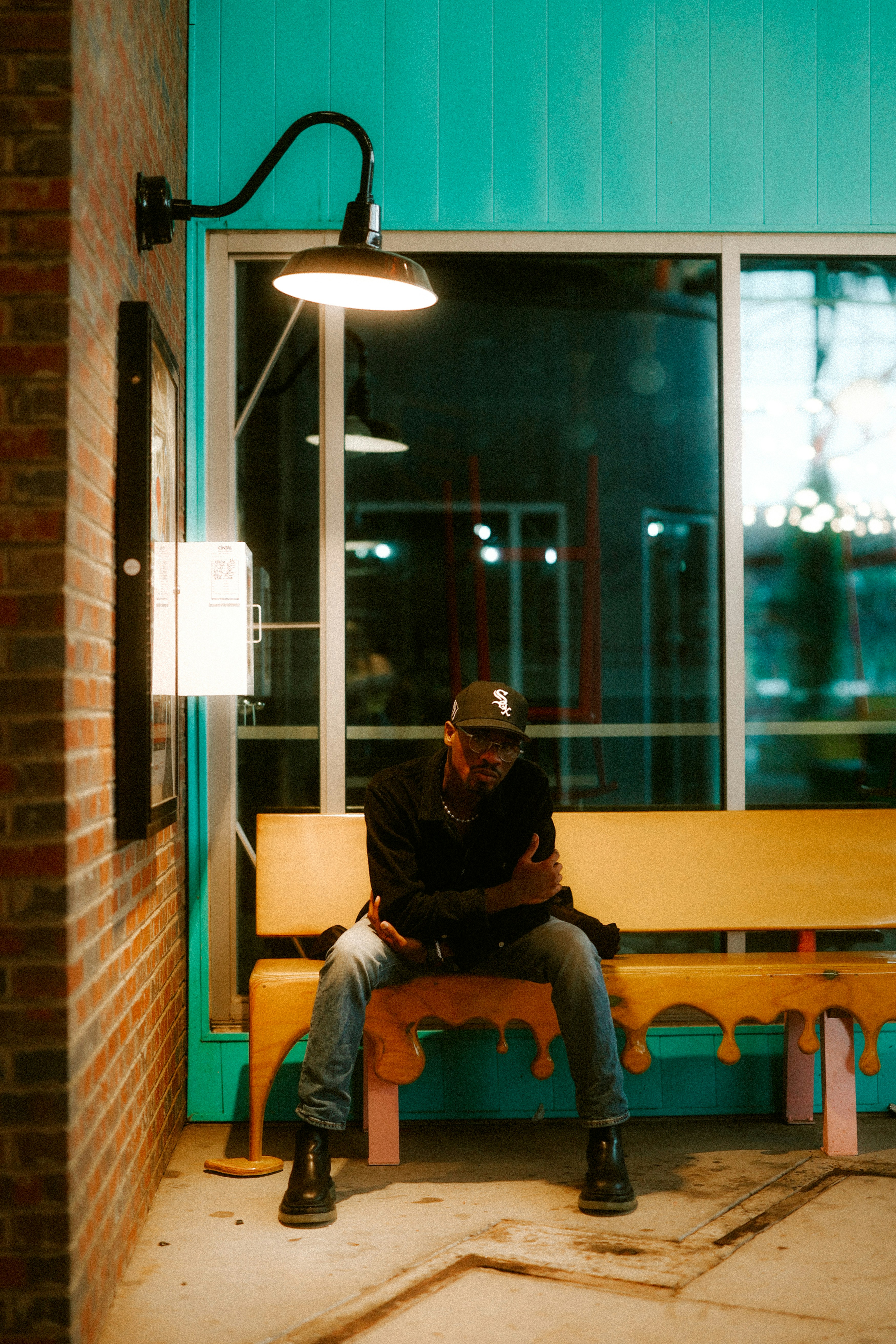 Quiet Pause on a Teal-Walled Bench Beneath a Warm Lamp