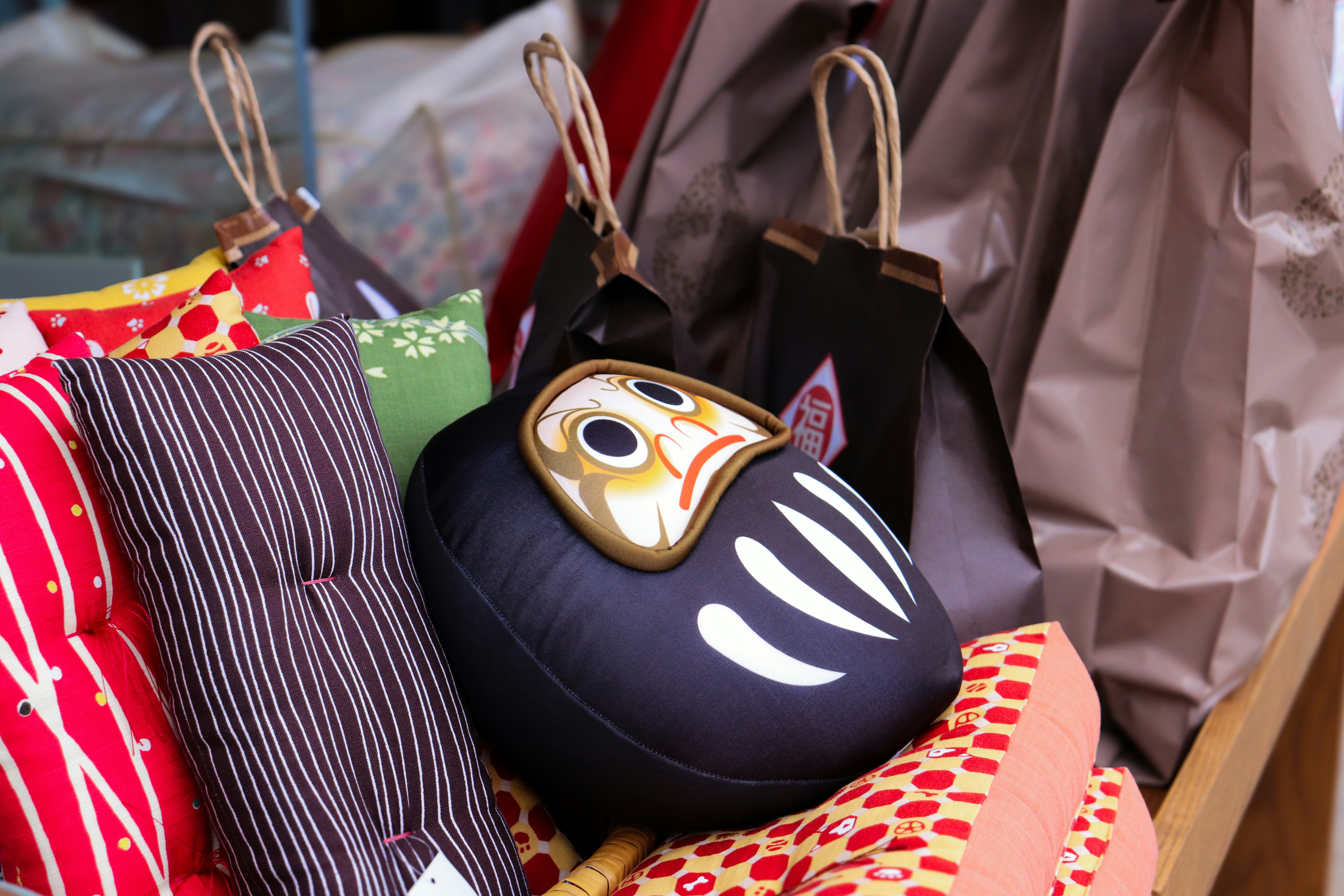 Colorful Display of Cushions and a Daruma Doll Pillow in a Japanese Souvenir Shop | Daruma doll among colorful cushions and bags.