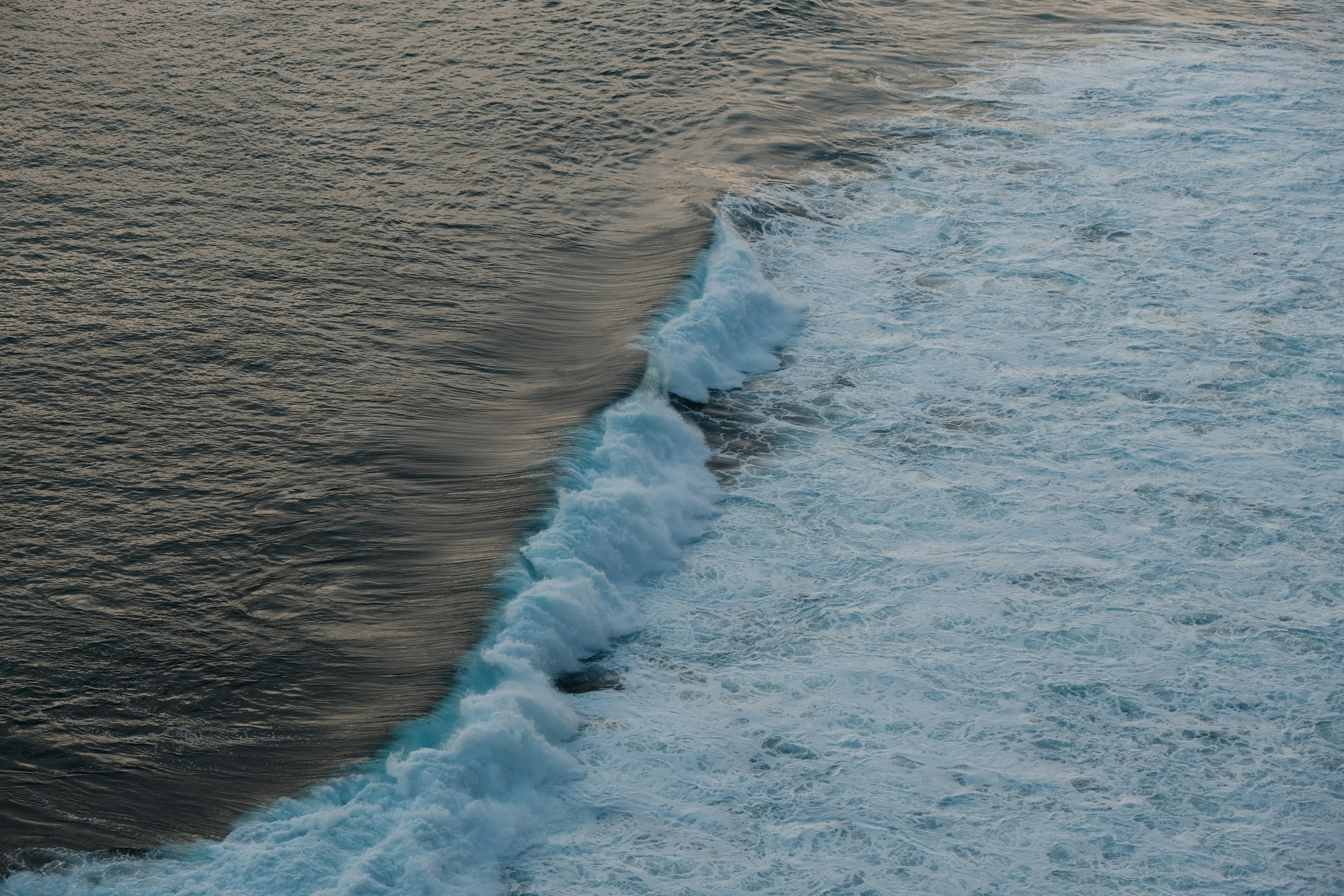 Gentle waves rolling onto a tranquil shoreline, blending hues of blue and gray under soft evening light.
