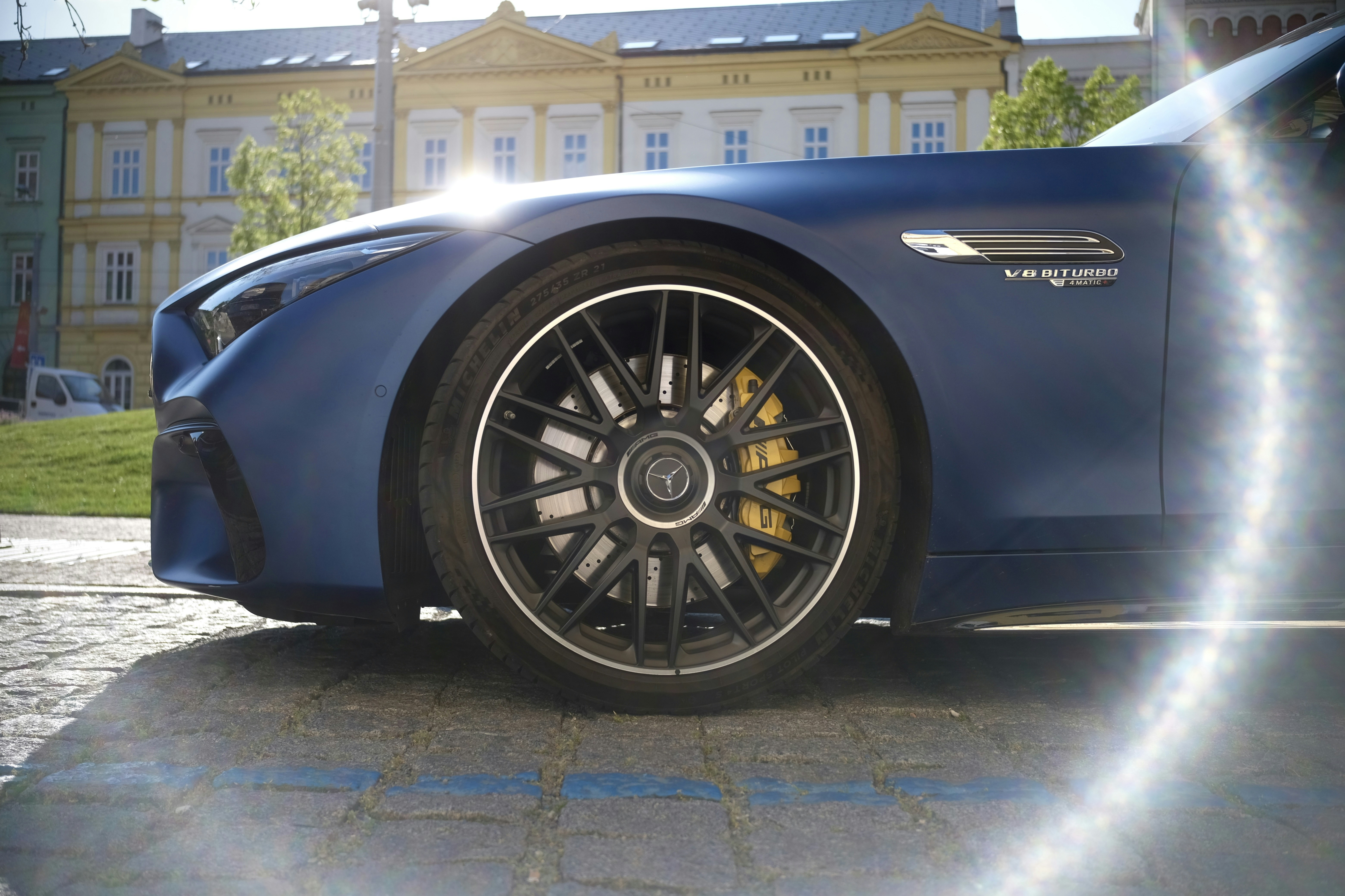 Blue performance wheel under sun glare: gold calipers and cobblestone backdrop