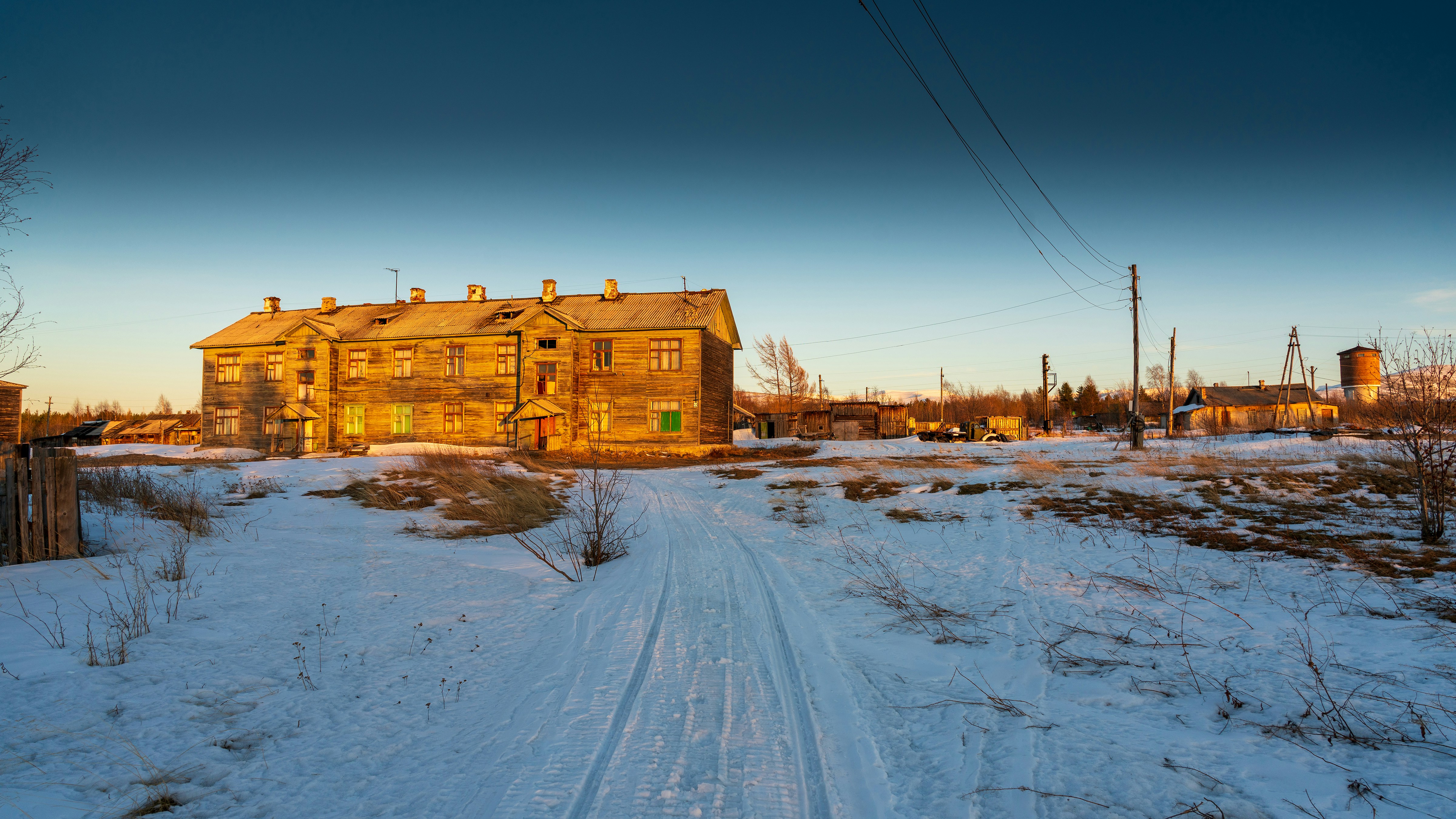 Abandoned wooden building bathed in golden light against a snowy landscape, hinting at stories of the past.
