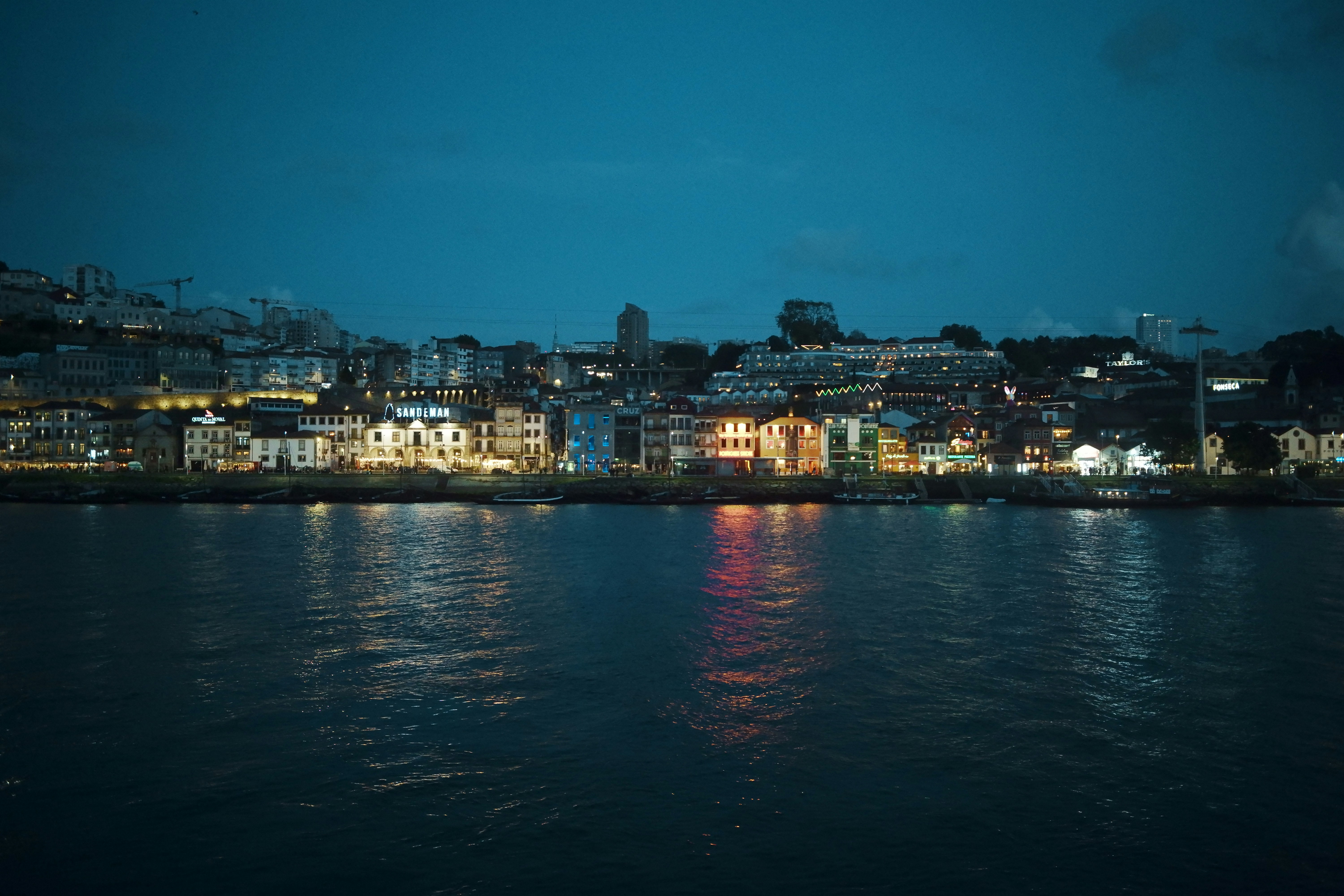 Illuminated waterfront buildings reflecting on calm waters during twilight, showcasing a blend of urban architecture and serene nature.