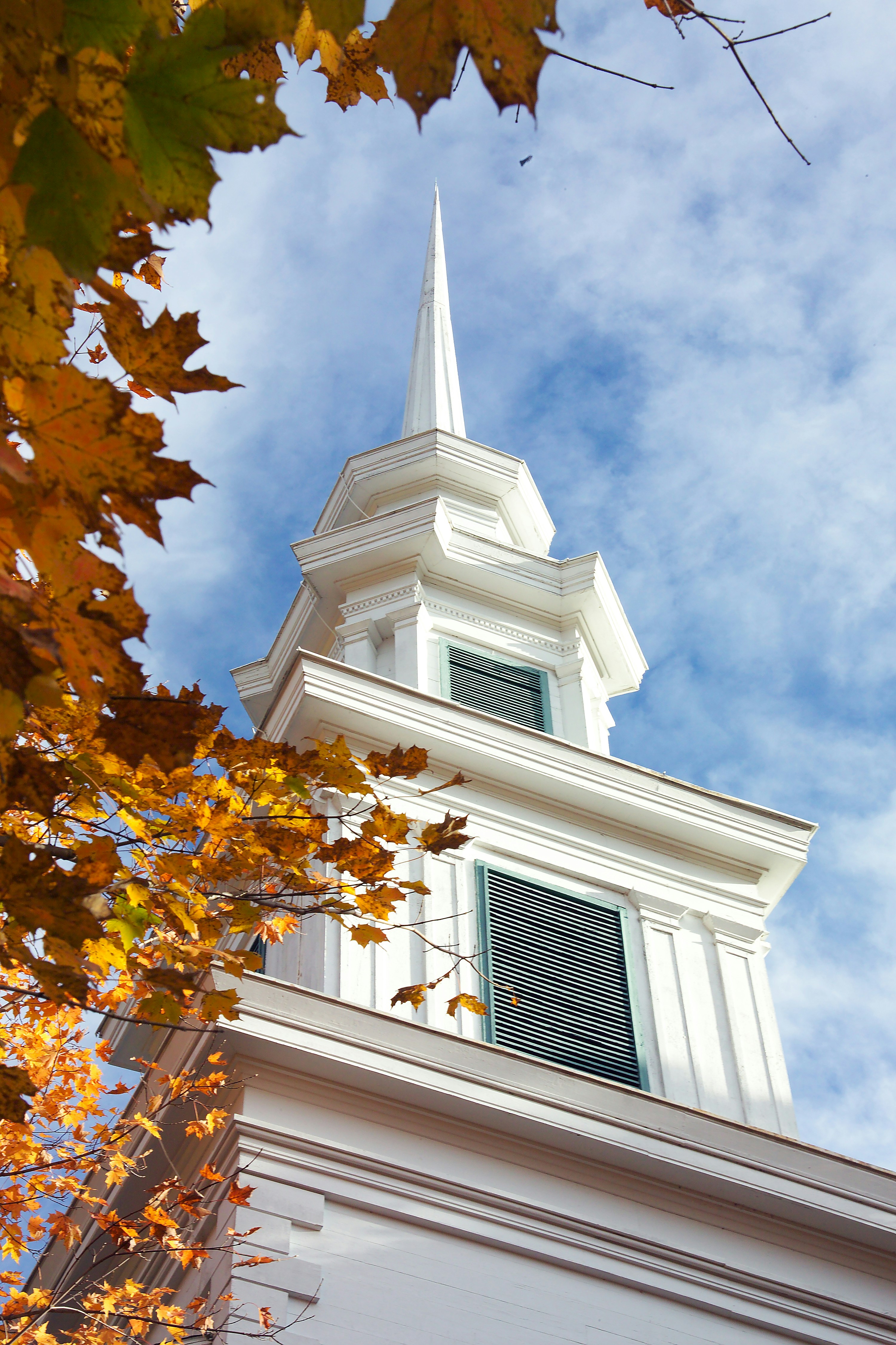 Spire Rising: Autumn Framing of a White Steeple Amid Fall Leaves