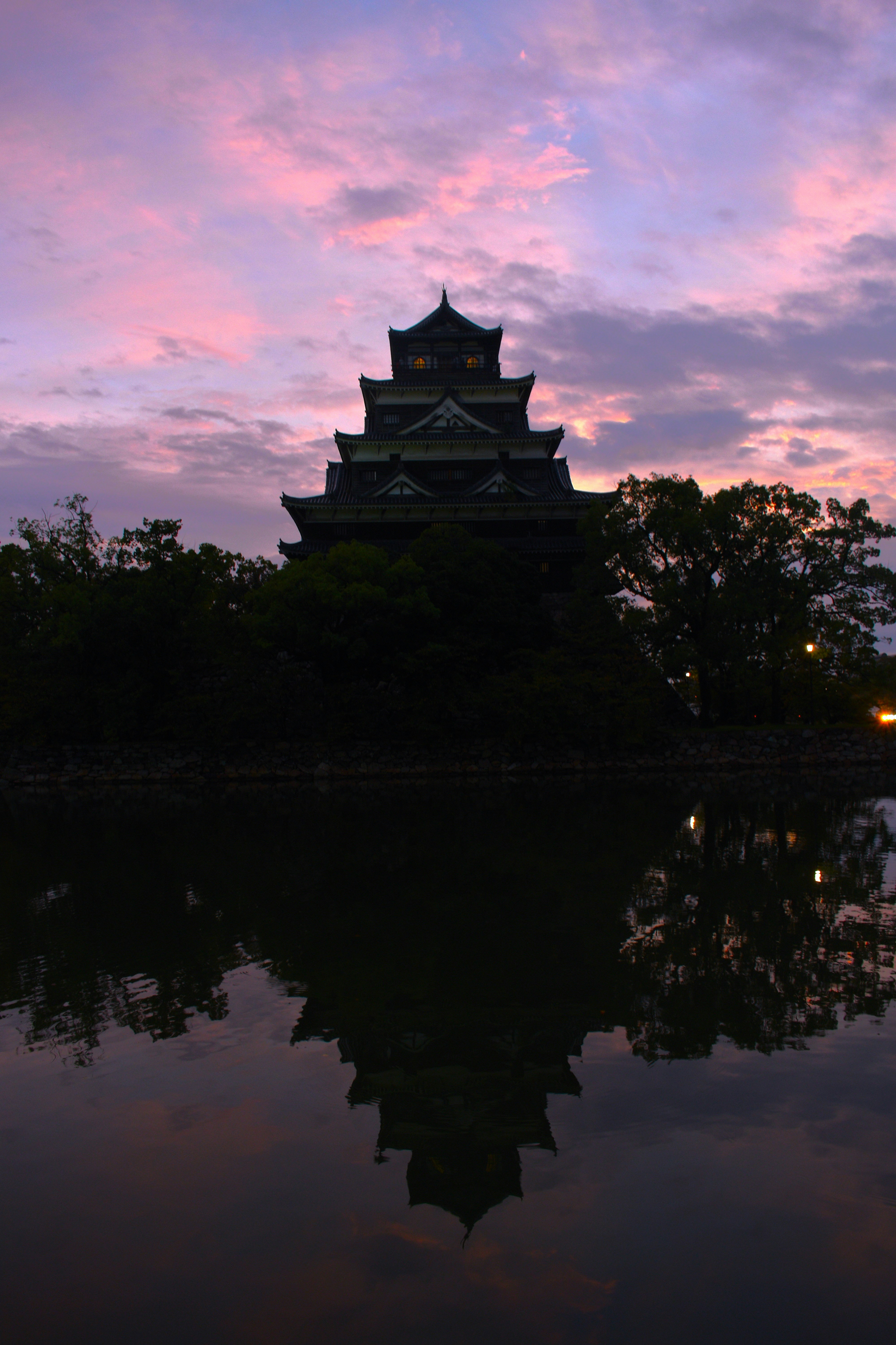 Historic castle silhouetted against a vibrant twilight sky, mirrored in the tranquil water below.