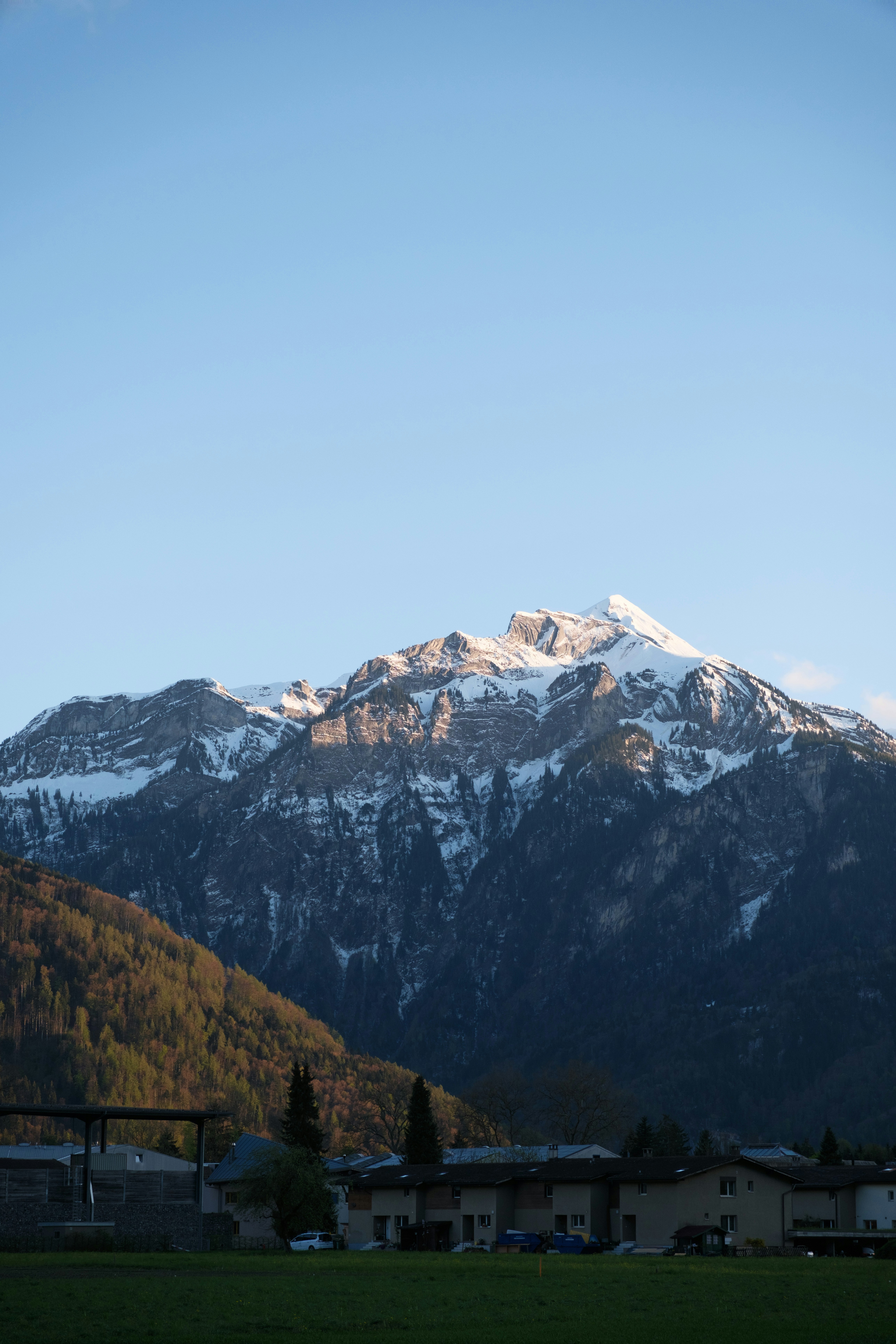 Snow-capped mountain range illuminated by the soft glow of evening light, contrasting with the lush valley below.