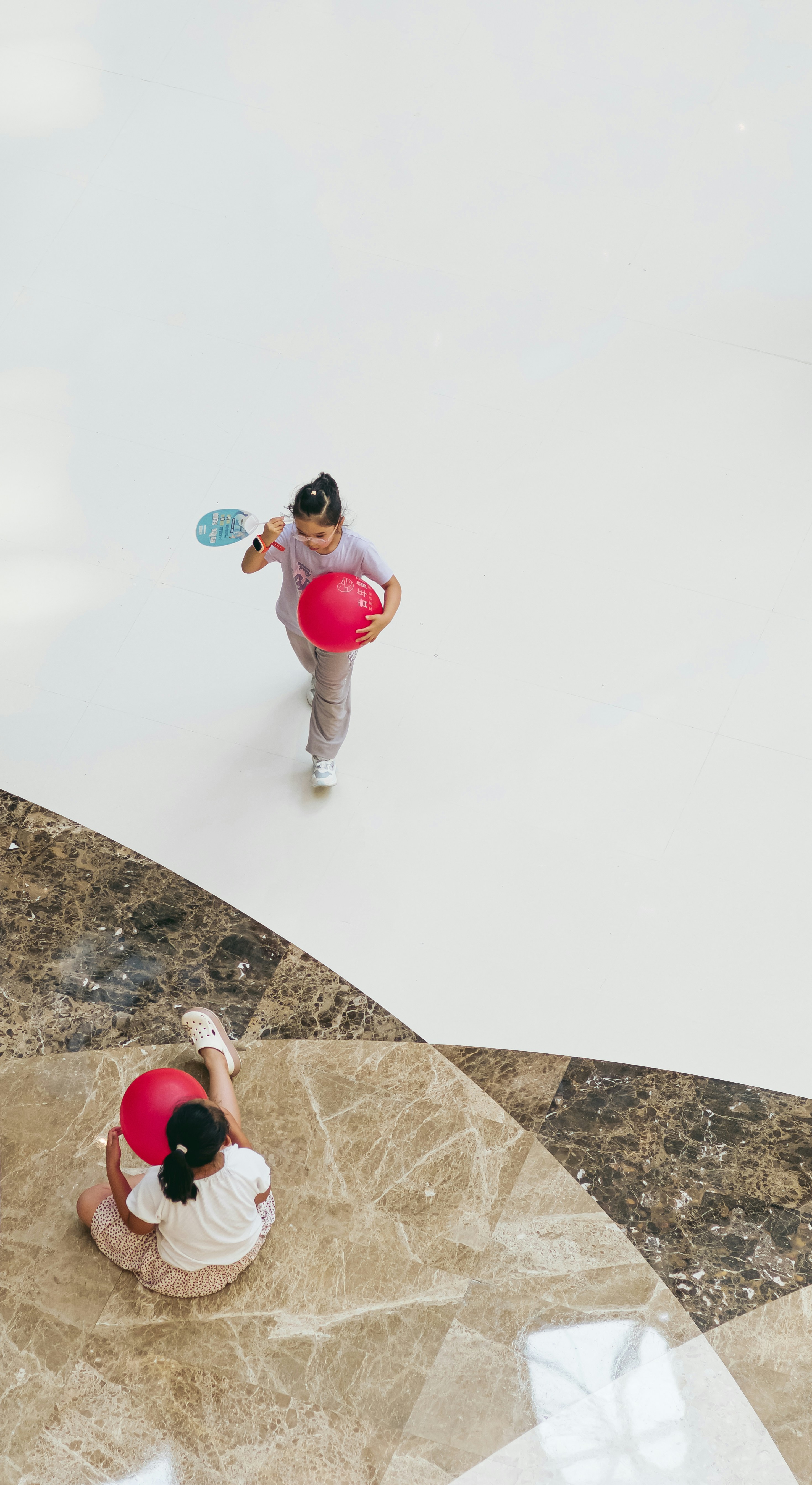 Elevated peek: a child with a pink ball alight in a vast atrial hush