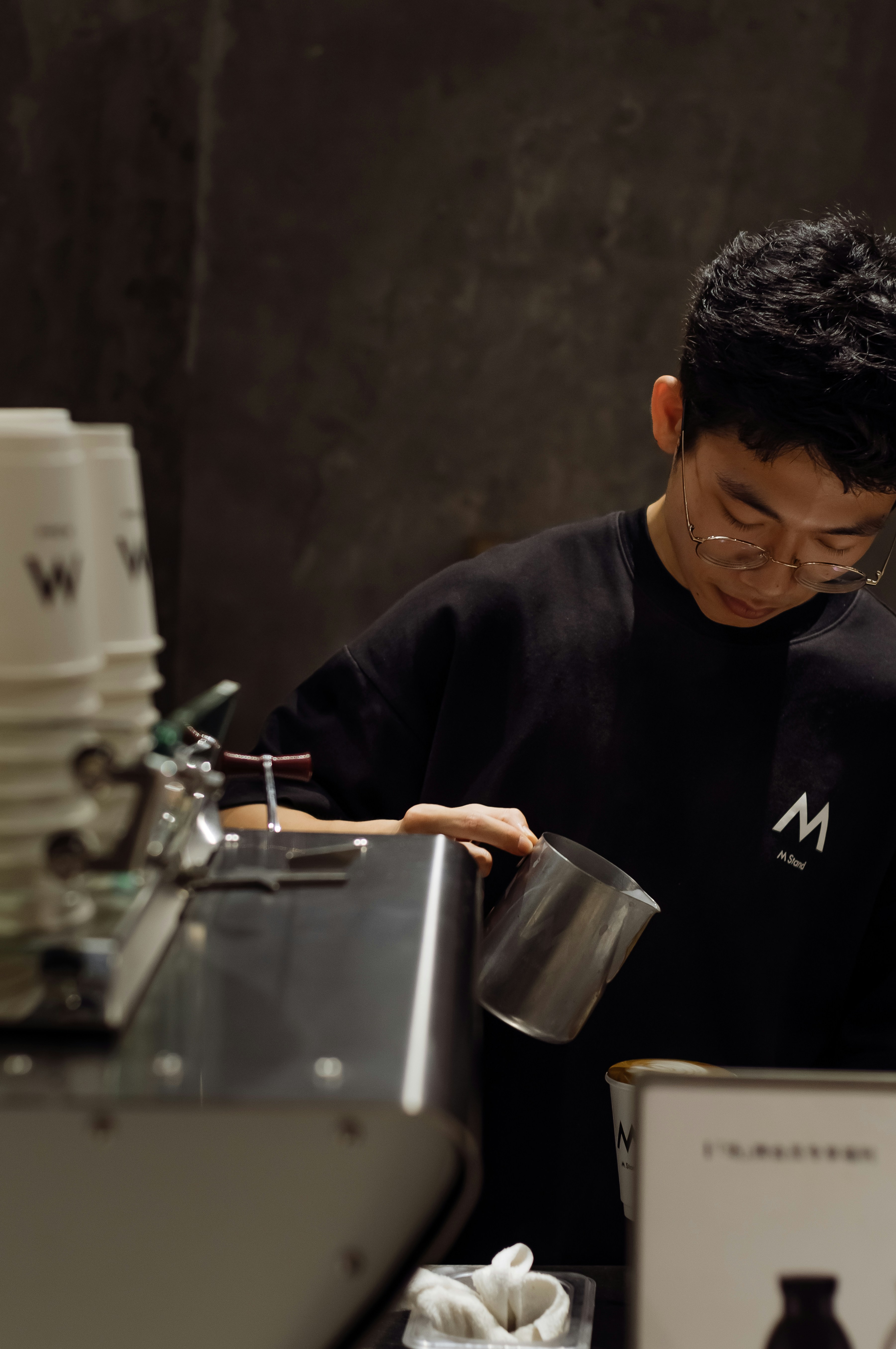 Barista pouring milk into a cup while concentrating on creating latte art in a modern café setting.