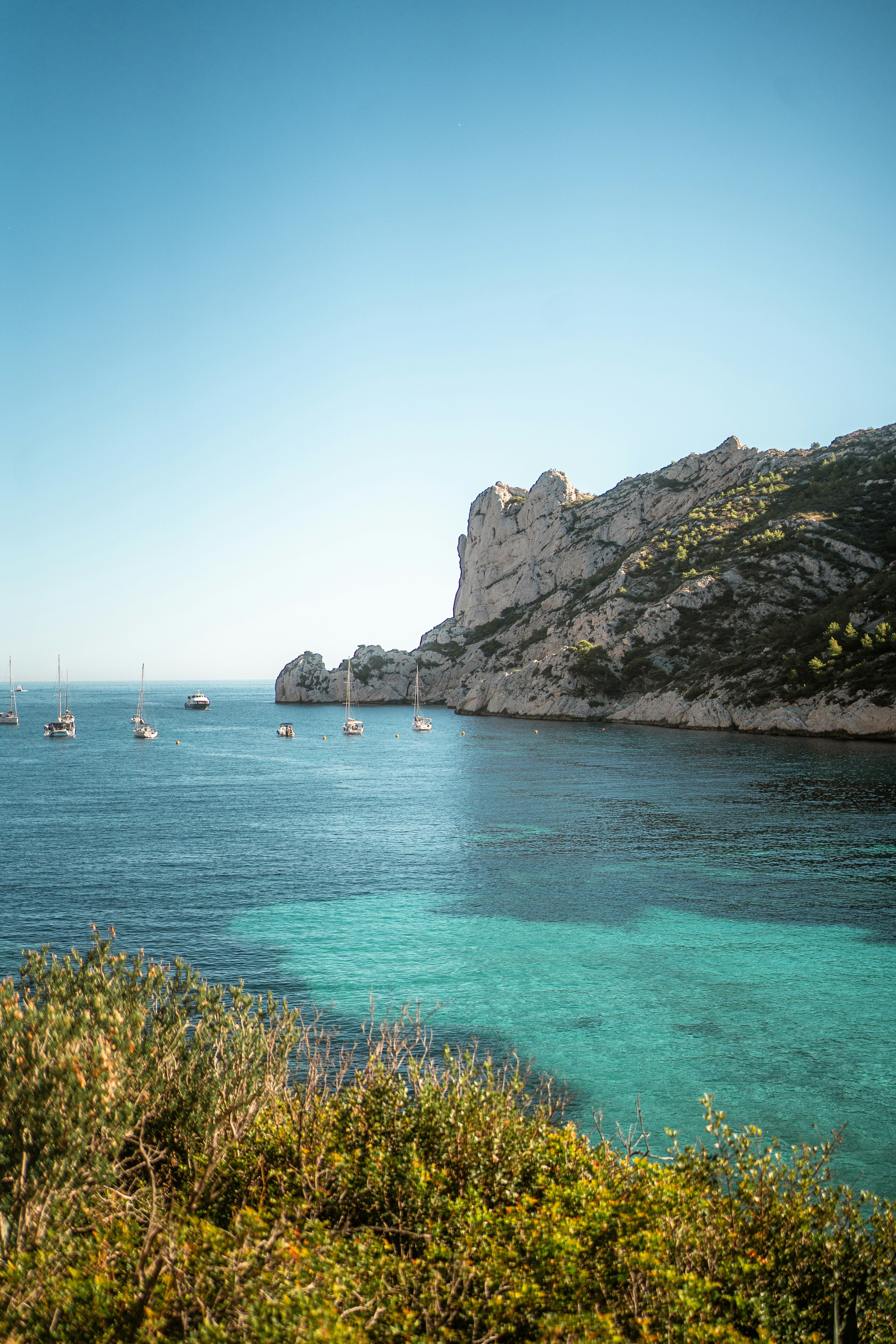 Boats sail in a turquoise cove near cliffs. photo – Free Beach Image on ...