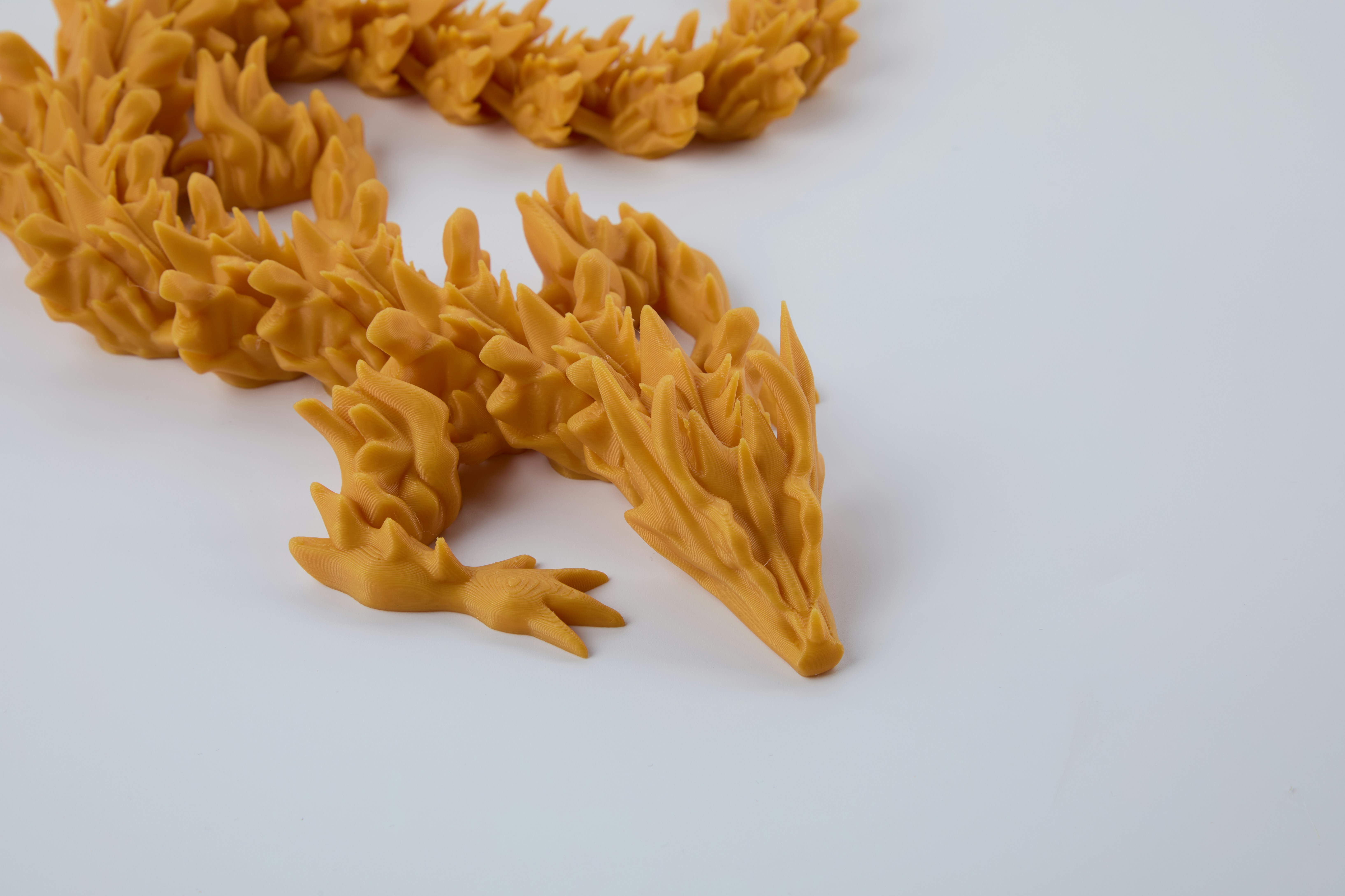A vibrant yellow dragon-like model with flame-shaped details, 3D printed using Snapmaker filament. | A golden, 3d-printed dragon is shown.