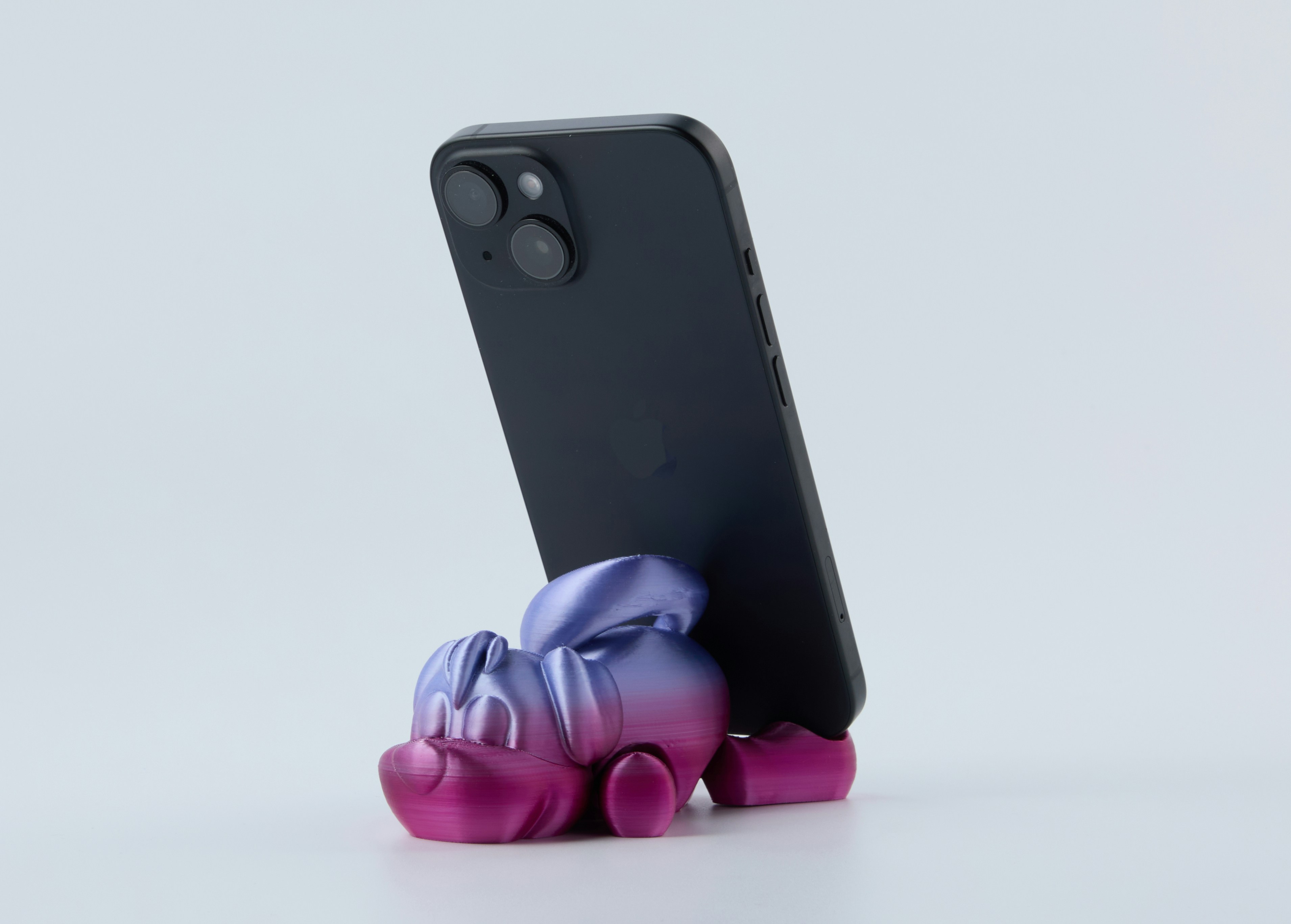 Form meets function—this gradient puppy serves as a phone holder, 3D printed with Snapmaker in dreamy violet tones. | A phone rests in a unique, colorful holder.
