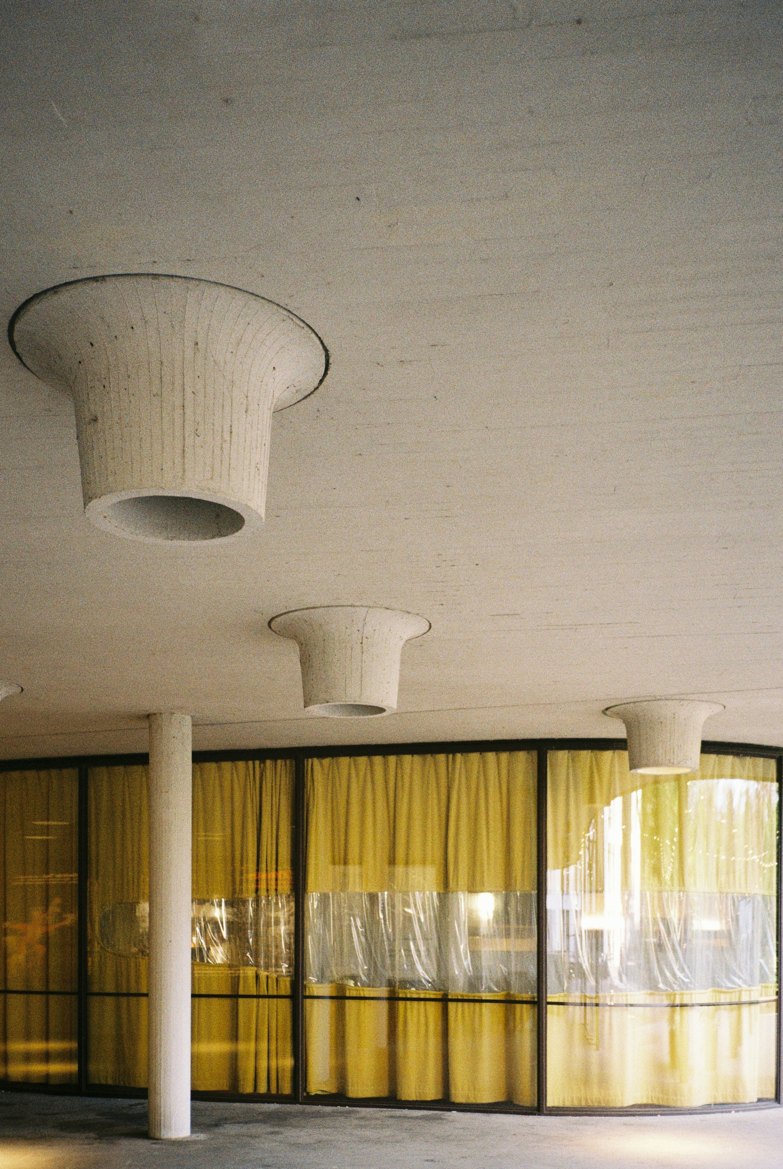 Concrete ceiling fixtures contrast with flowing yellow curtains, creating a unique interplay of shapes and colors in a modern architectural space.