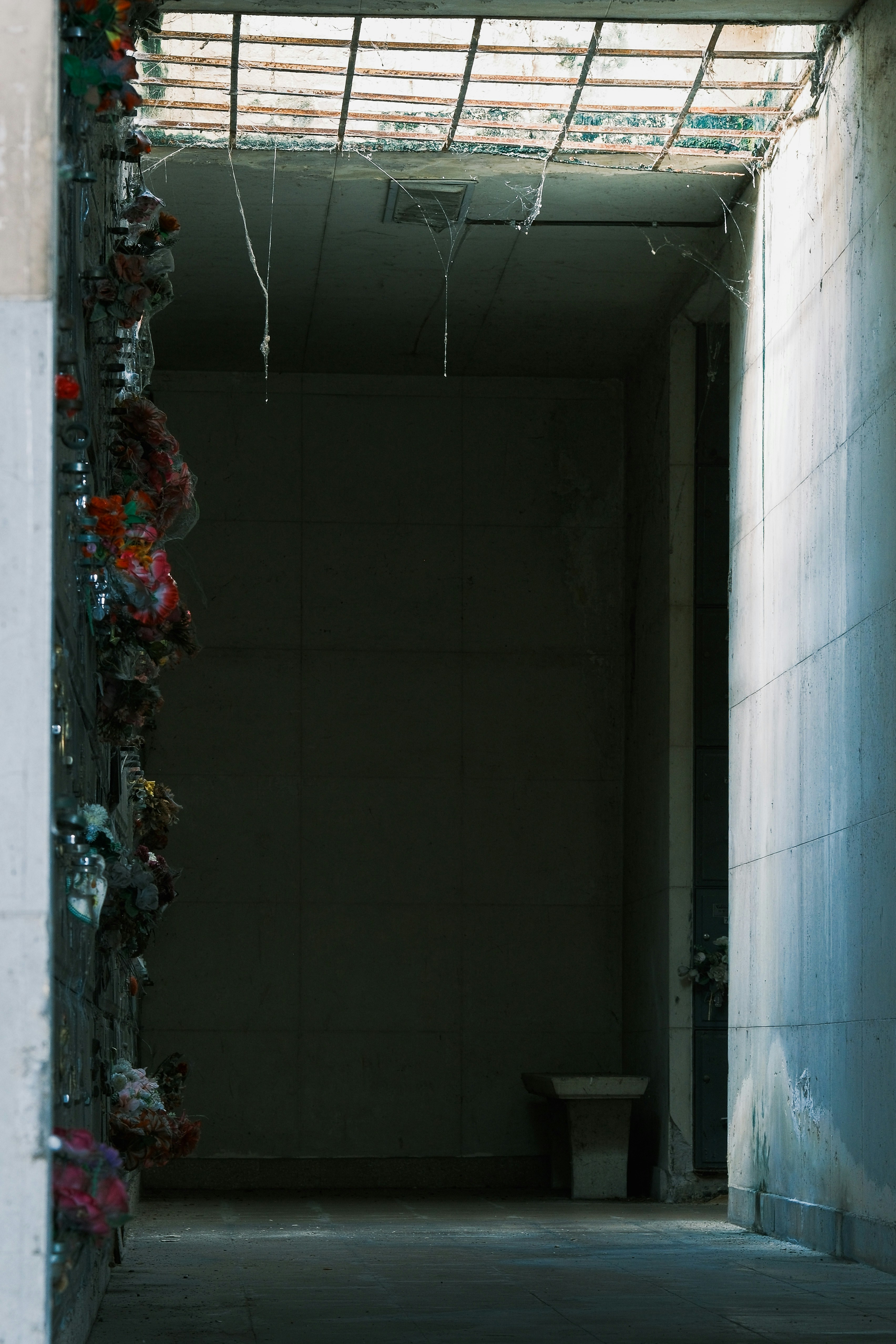 Spider webs hanging from a broken ceiling inside a mausoleum, with flower offerings fading away in silence.