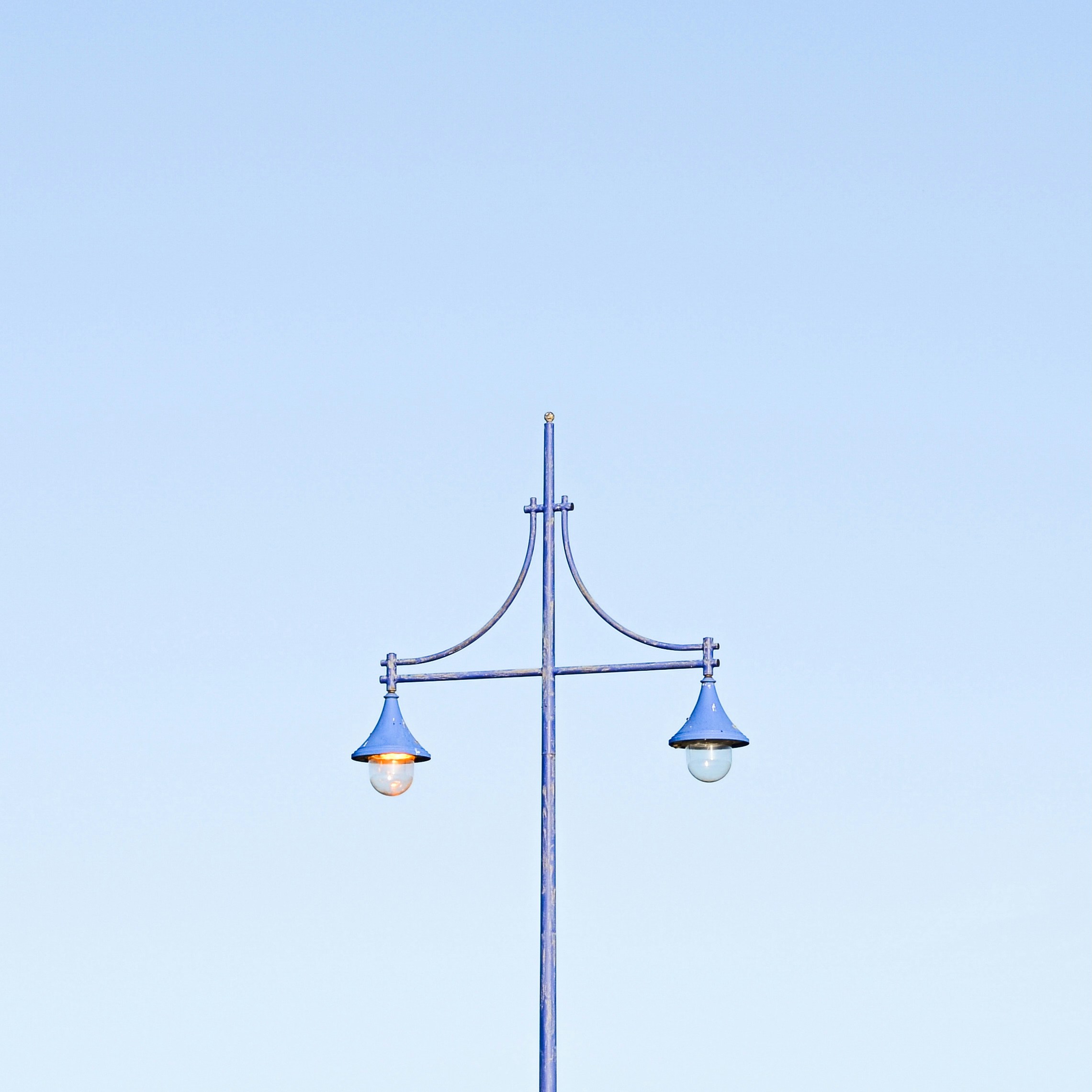 Vintage street lamp with two differently colored bulbs against a clear blue sky.