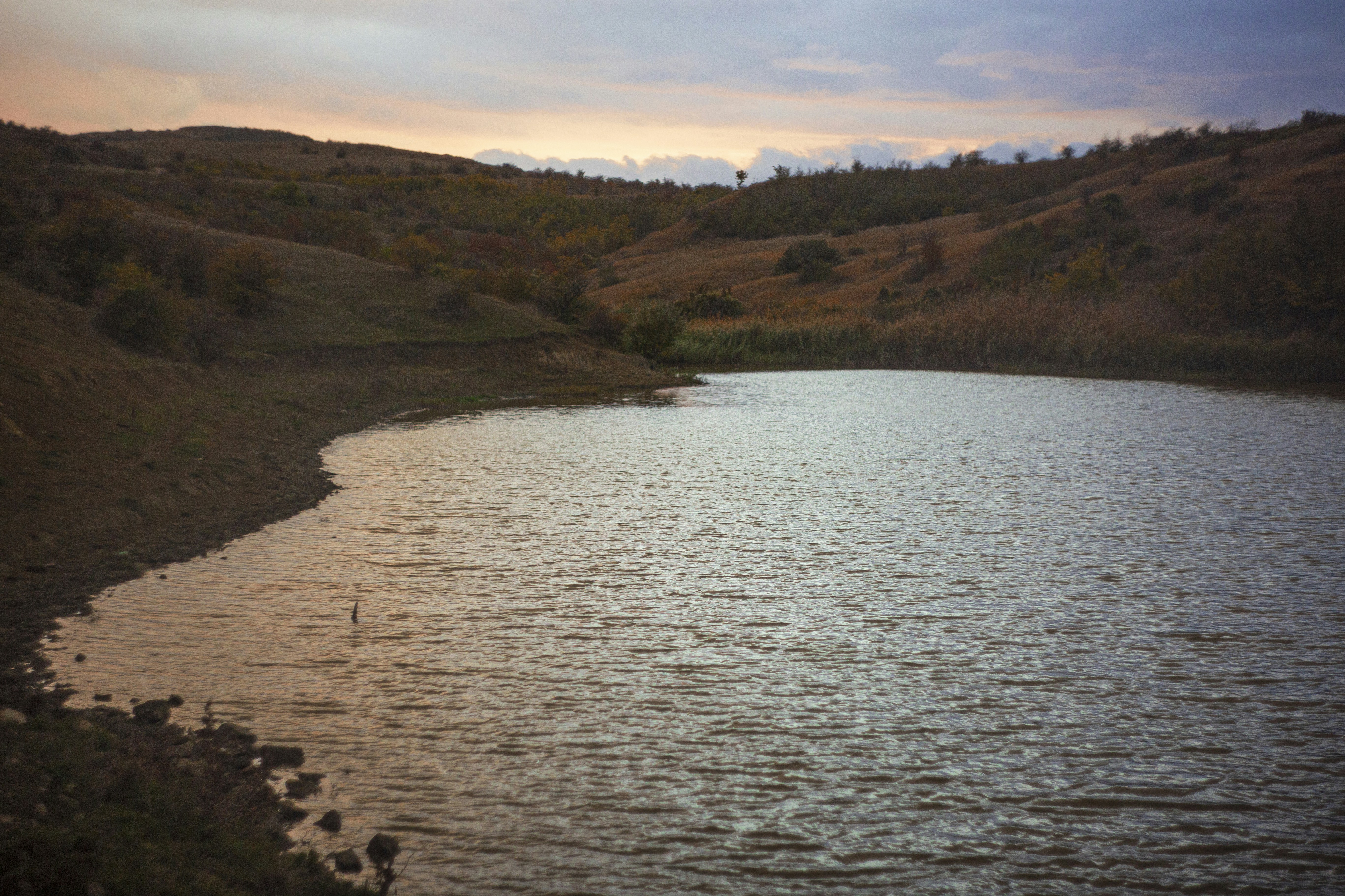 Gentle ripples on a serene lake surrounded by rolling hills under a soft twilight sky.