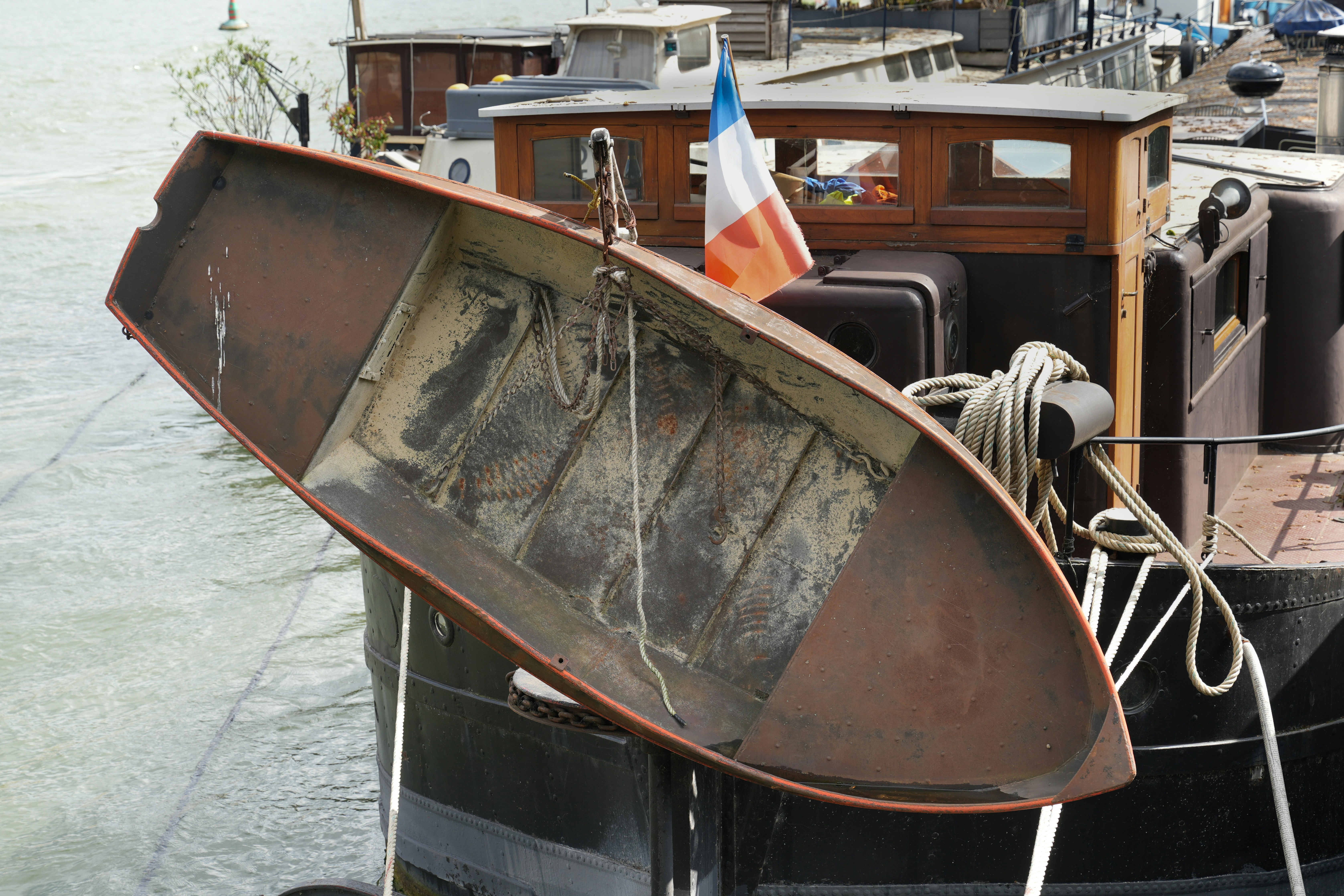 Rusted Dinghy Perched Across a Classic Barge Beneath a Flapping French Flag
