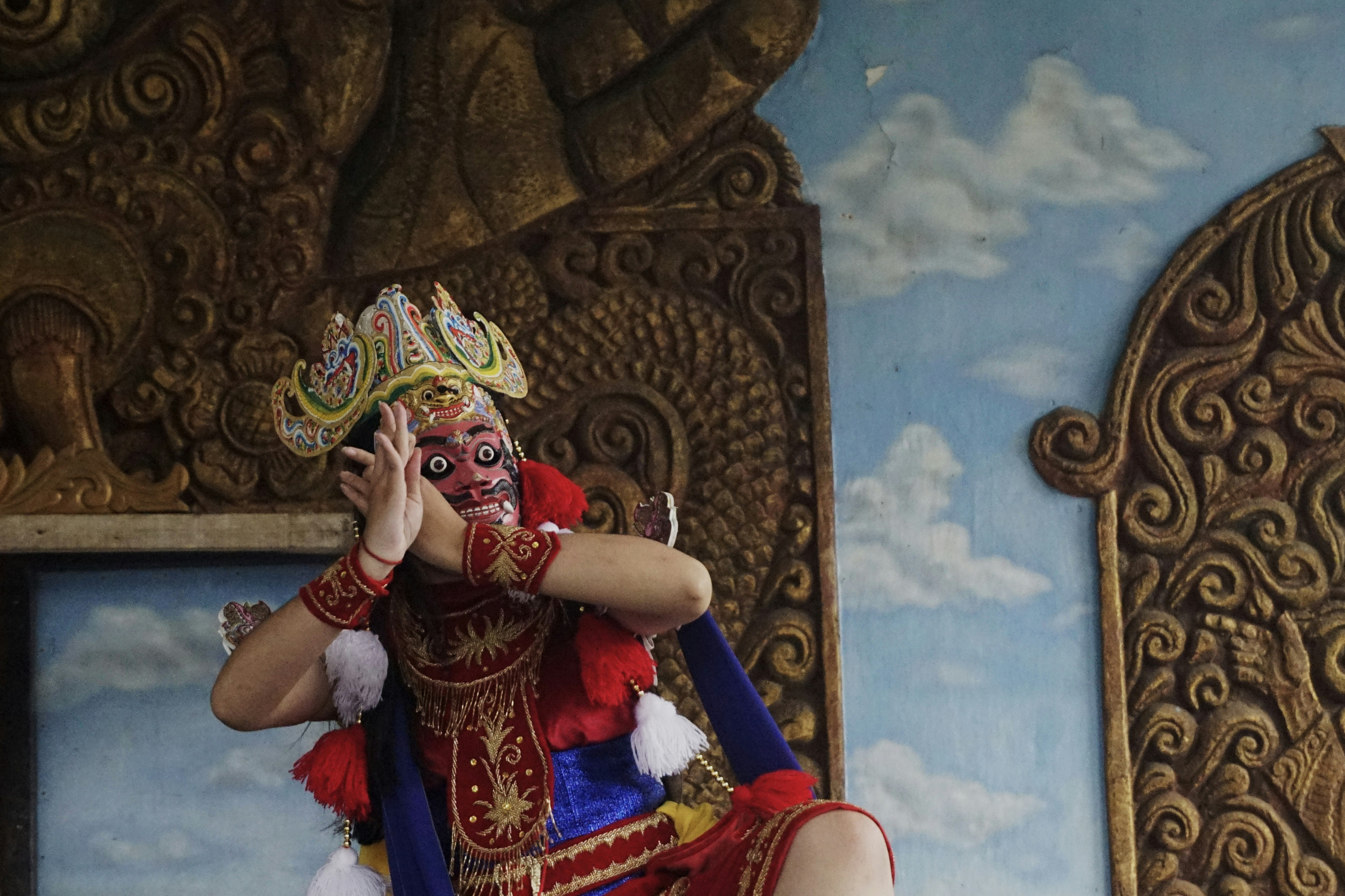 Traditional performer in elaborate costume and makeup, showcasing a dramatic pose against a vibrant backdrop.