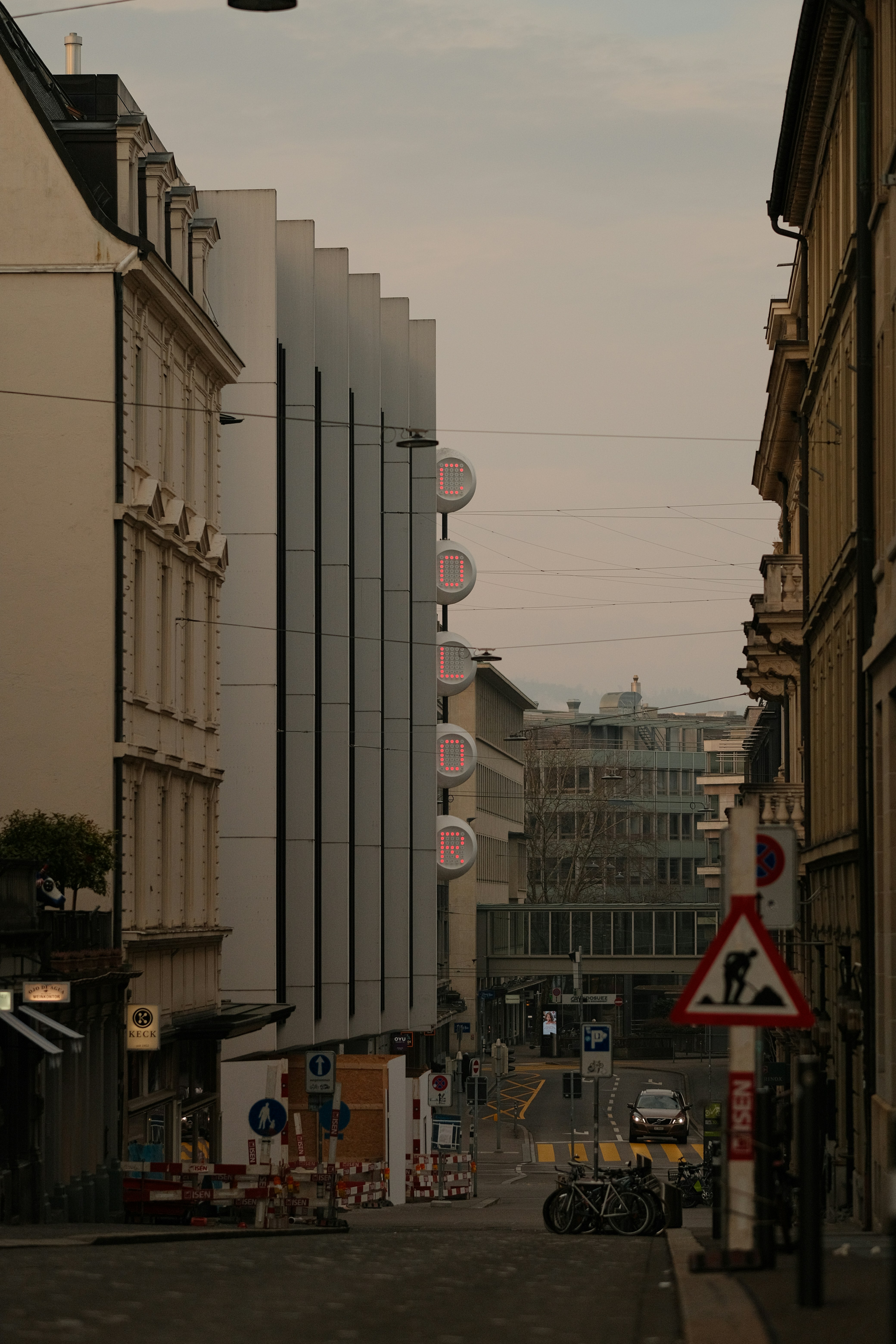 A narrow street scene showcasing a blend of historical architecture and contemporary design, with traffic signs and a distant building illuminated by soft light.