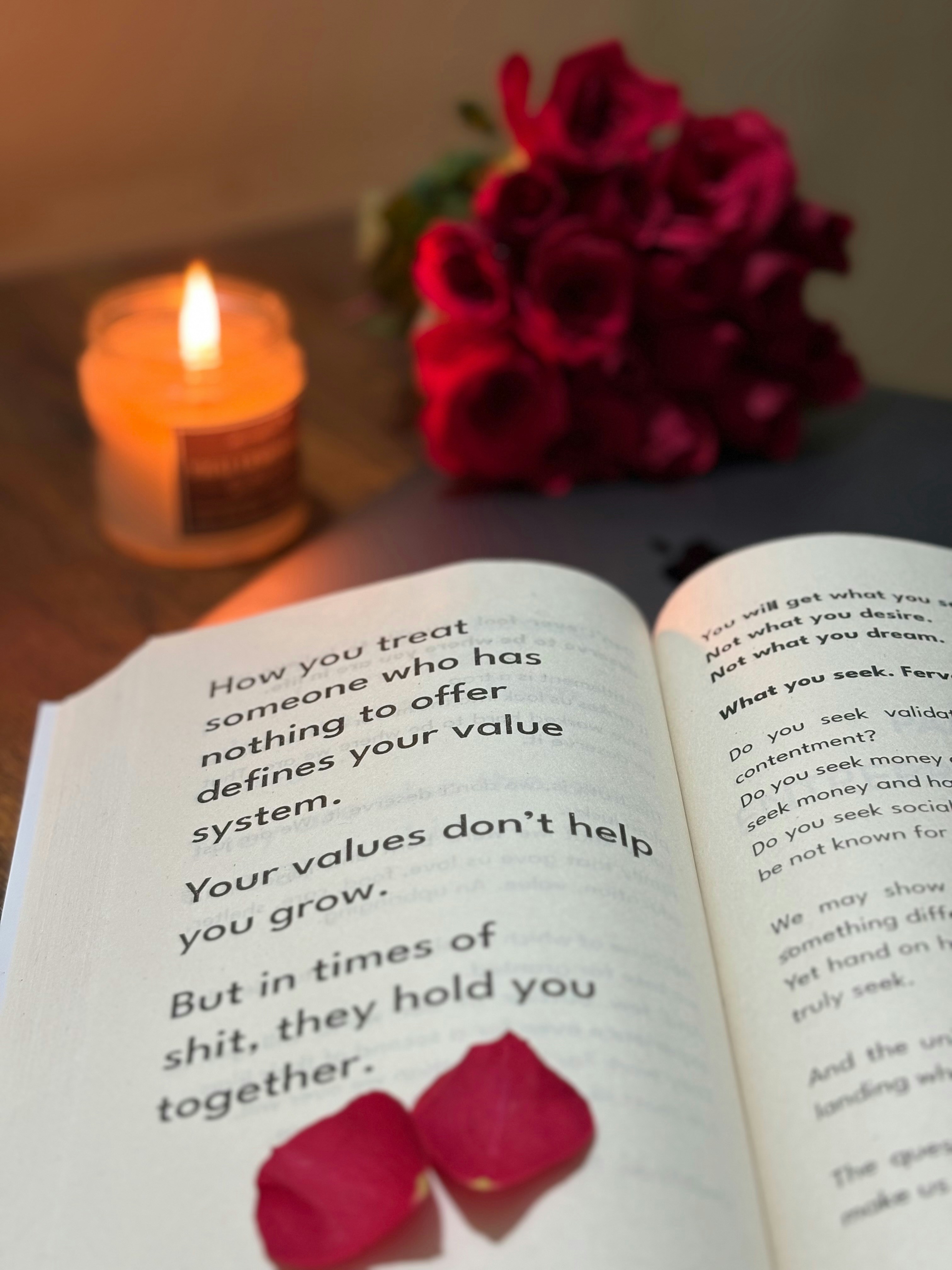 Open book displaying thoughtful text on personal values with rose petals and a lit candle in the background.