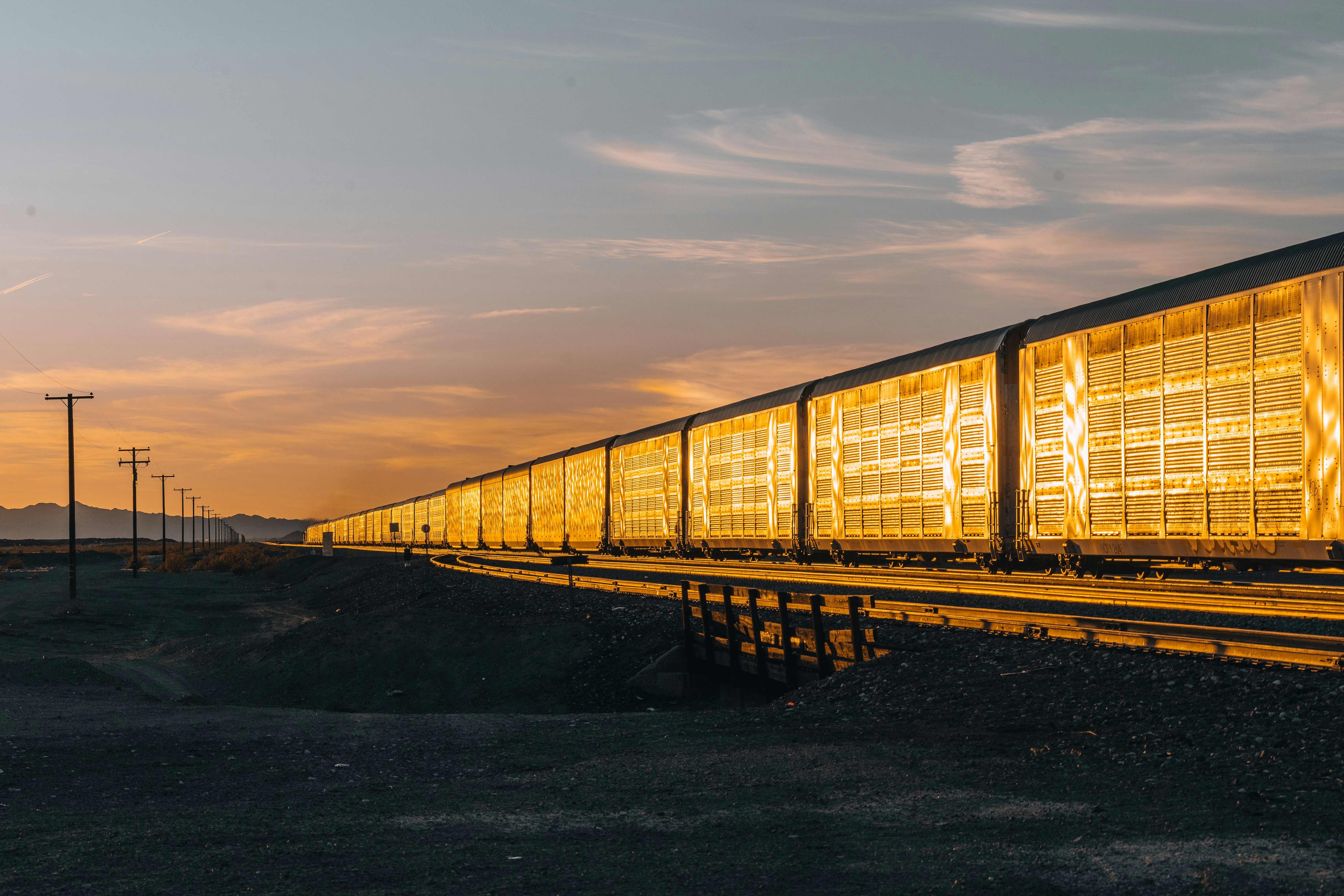 A freight train illuminated by the warm glow of sunset, stretching along the tracks with a backdrop of a serene sky. The scene captures the essence of travel and industry.
