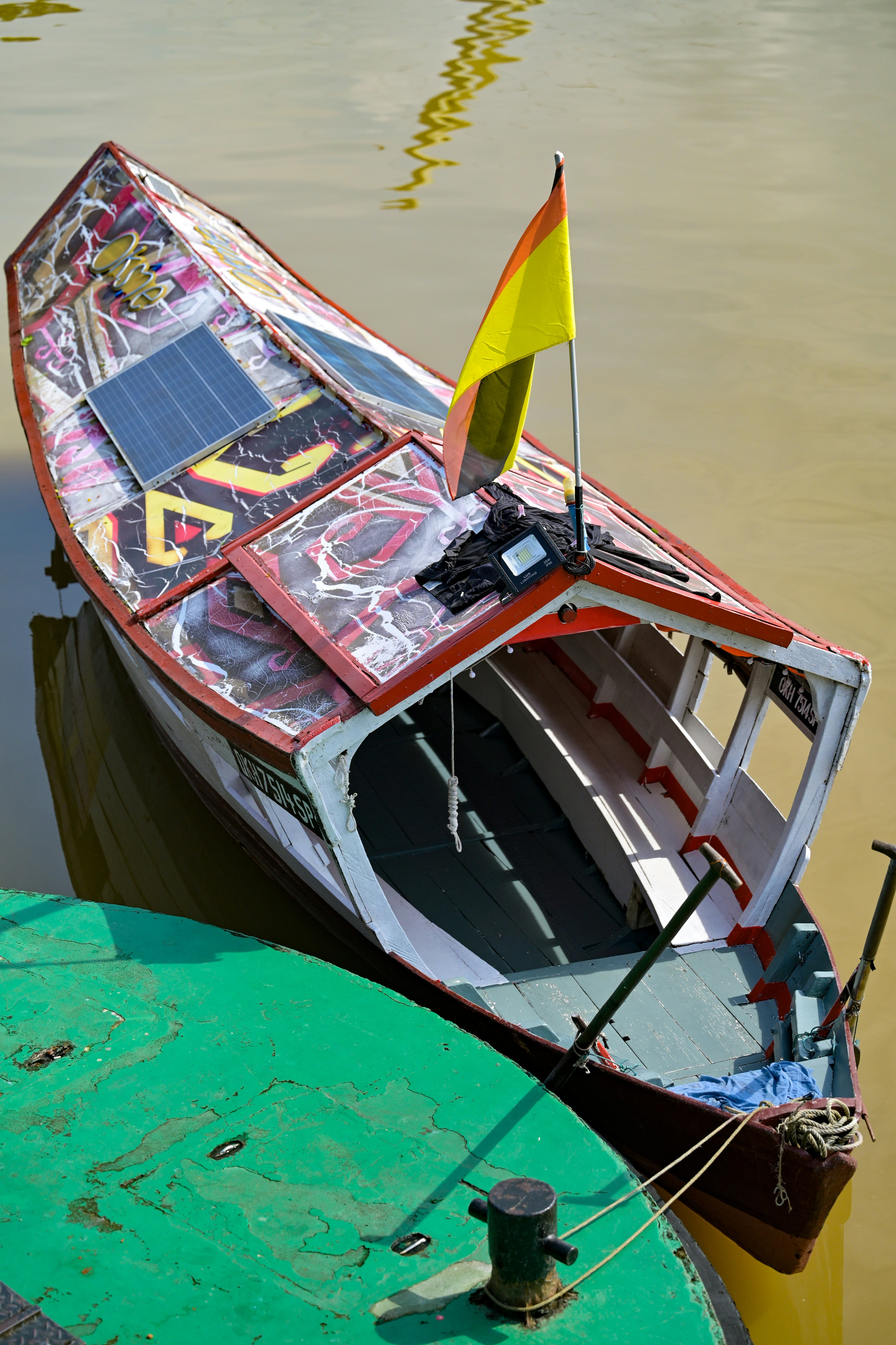 Tilted Graffiti Boat with Solar Panel and Flag on a Quiet River