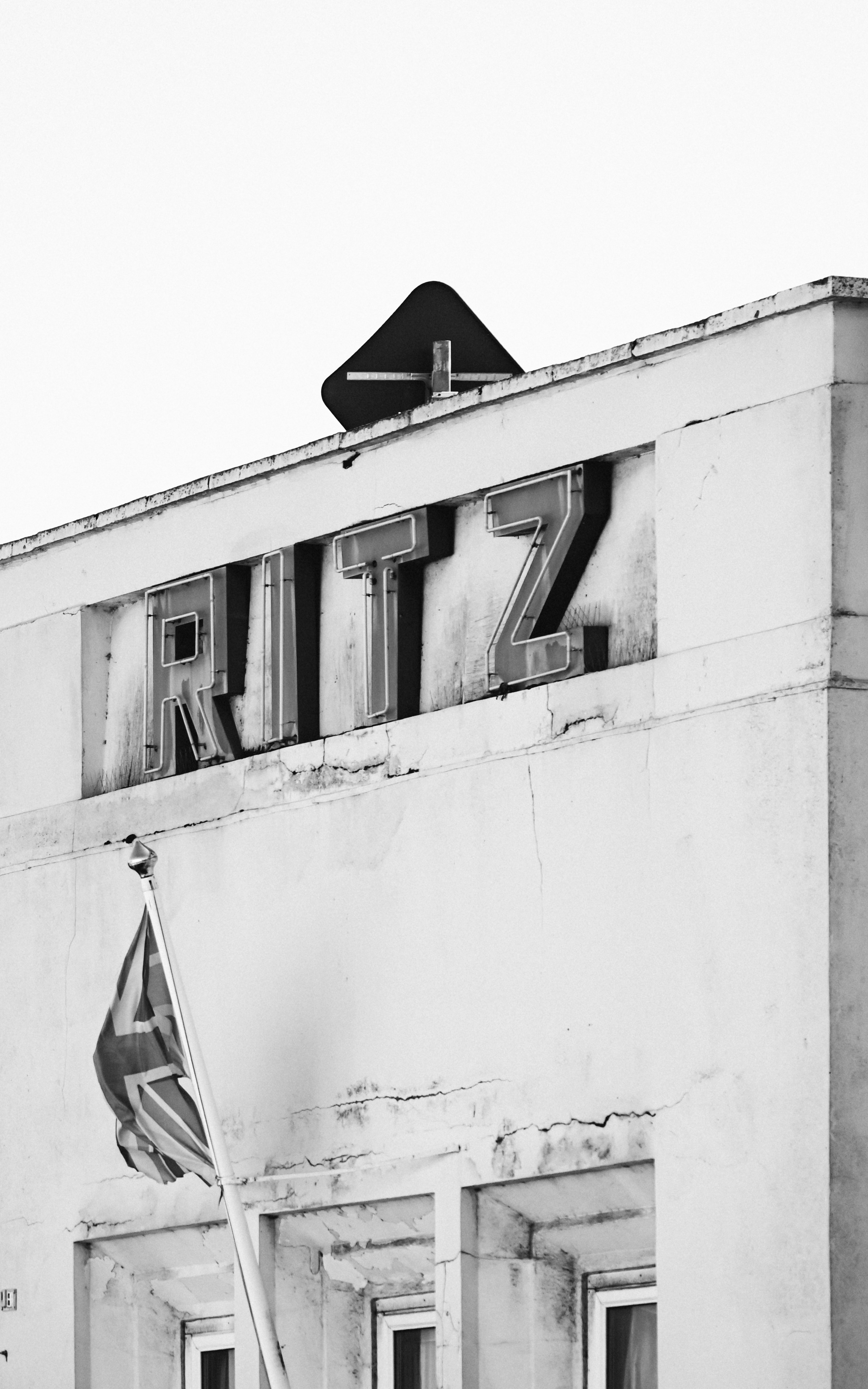 Weathered Ritz sign against a stark sky, with a British flag fluttering below. The contrast highlights the building's historical charm.