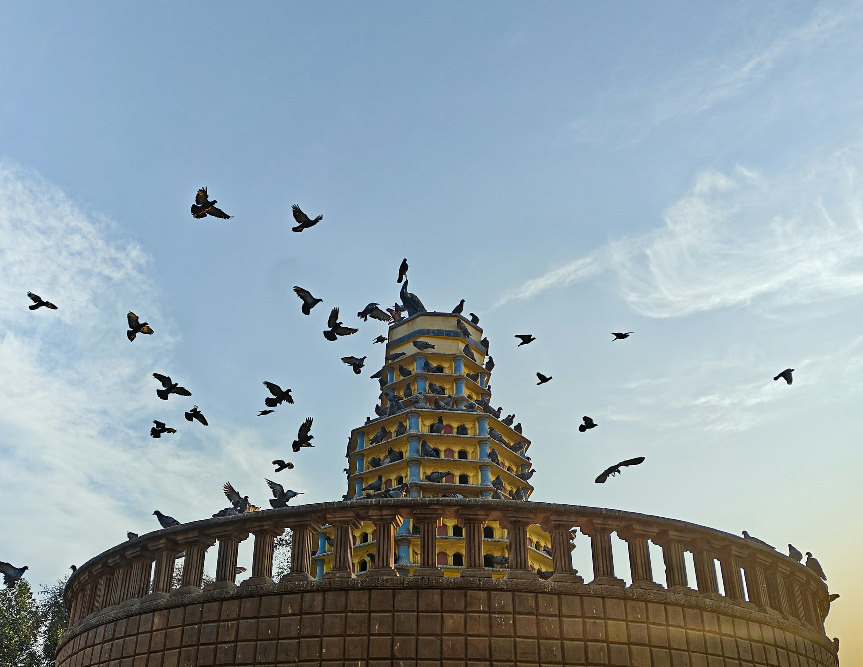 Colorful tower adorned with birds in flight against a clear sky, showcasing a lively interaction between nature and structure.