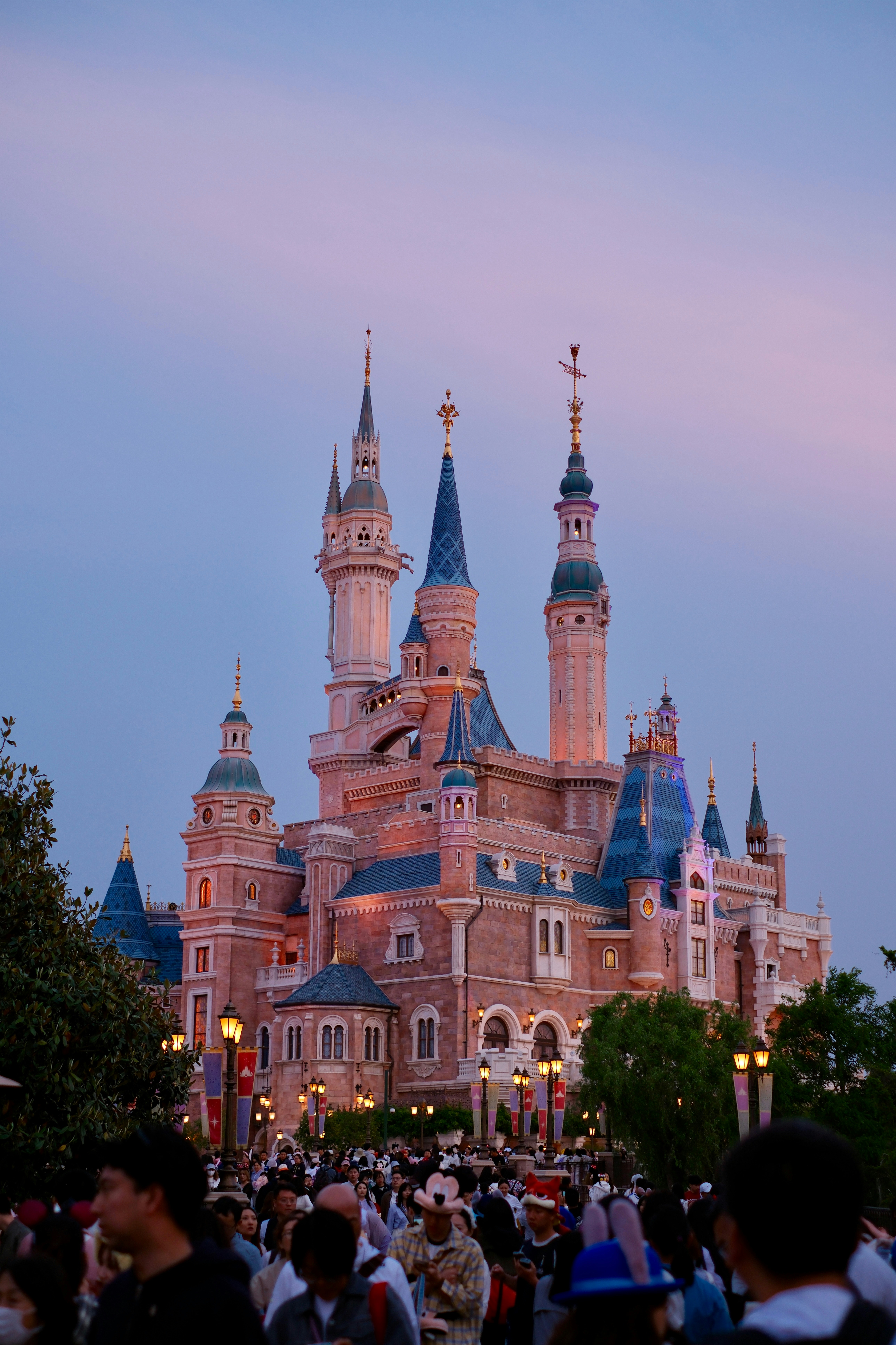 Disney castle at dusk, crowded with people.