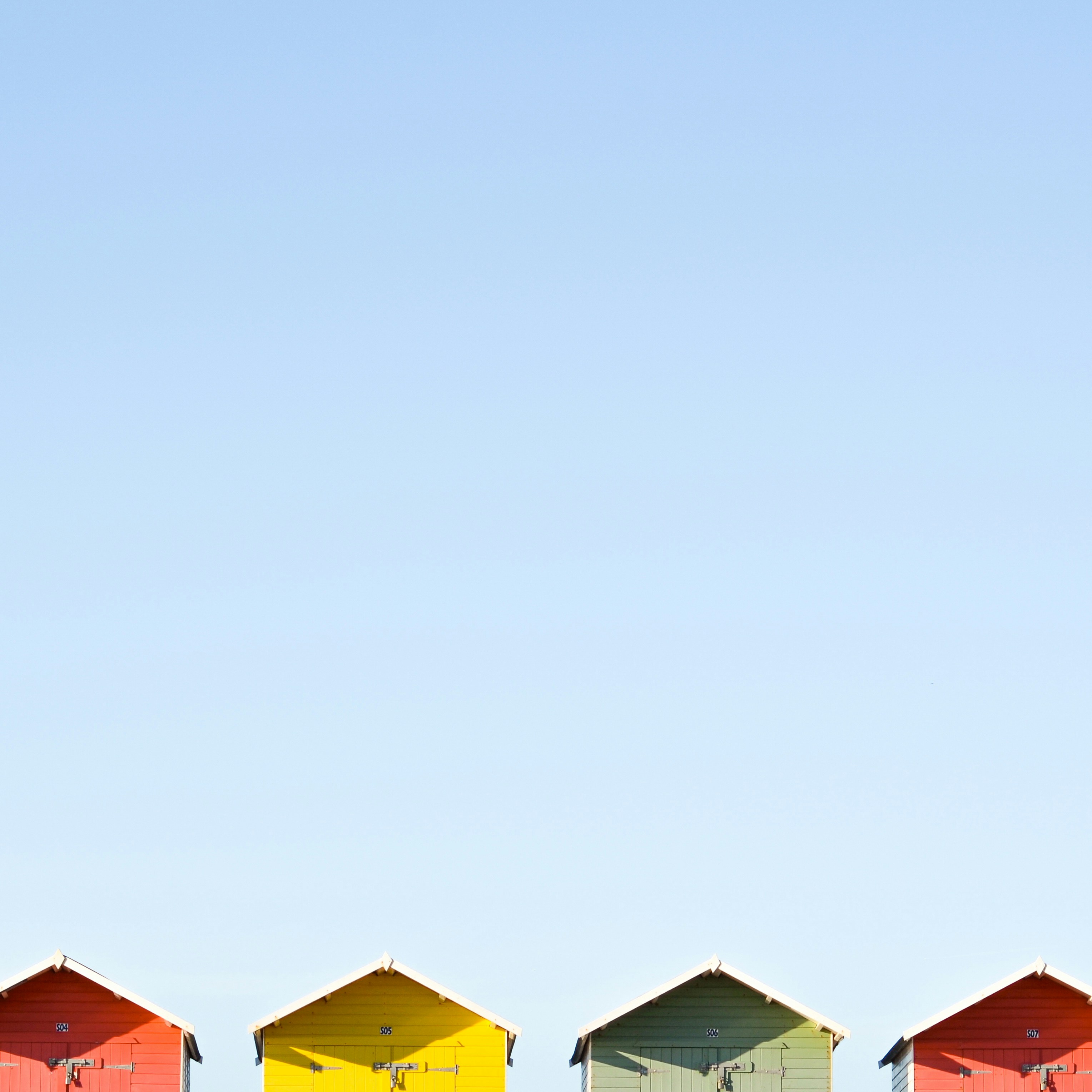 Colorful beach huts are arranged under a clear, blue sky.