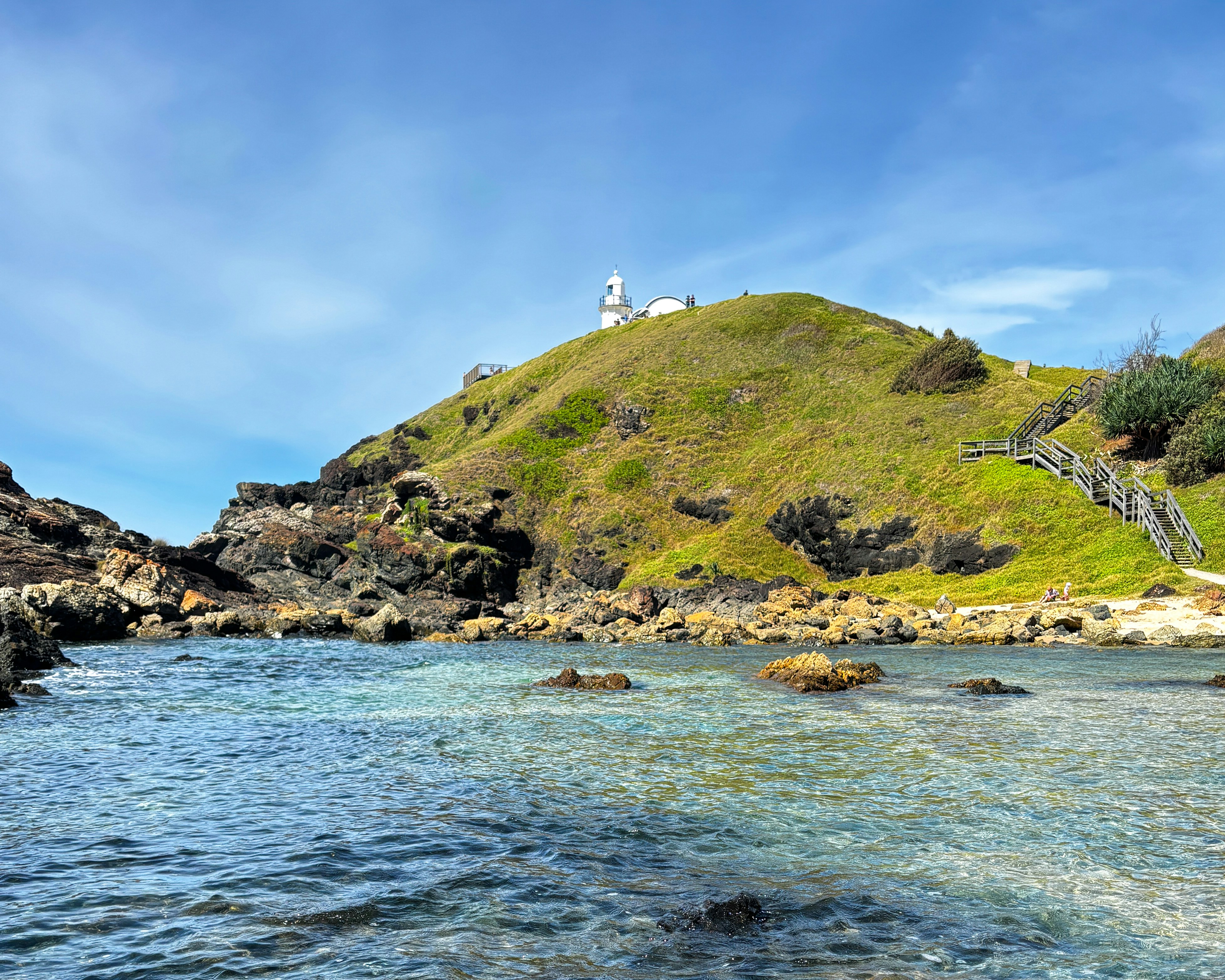 A serene coastal scene featuring a lighthouse perched on a verdant hill, surrounded by rocky shores and clear waters.