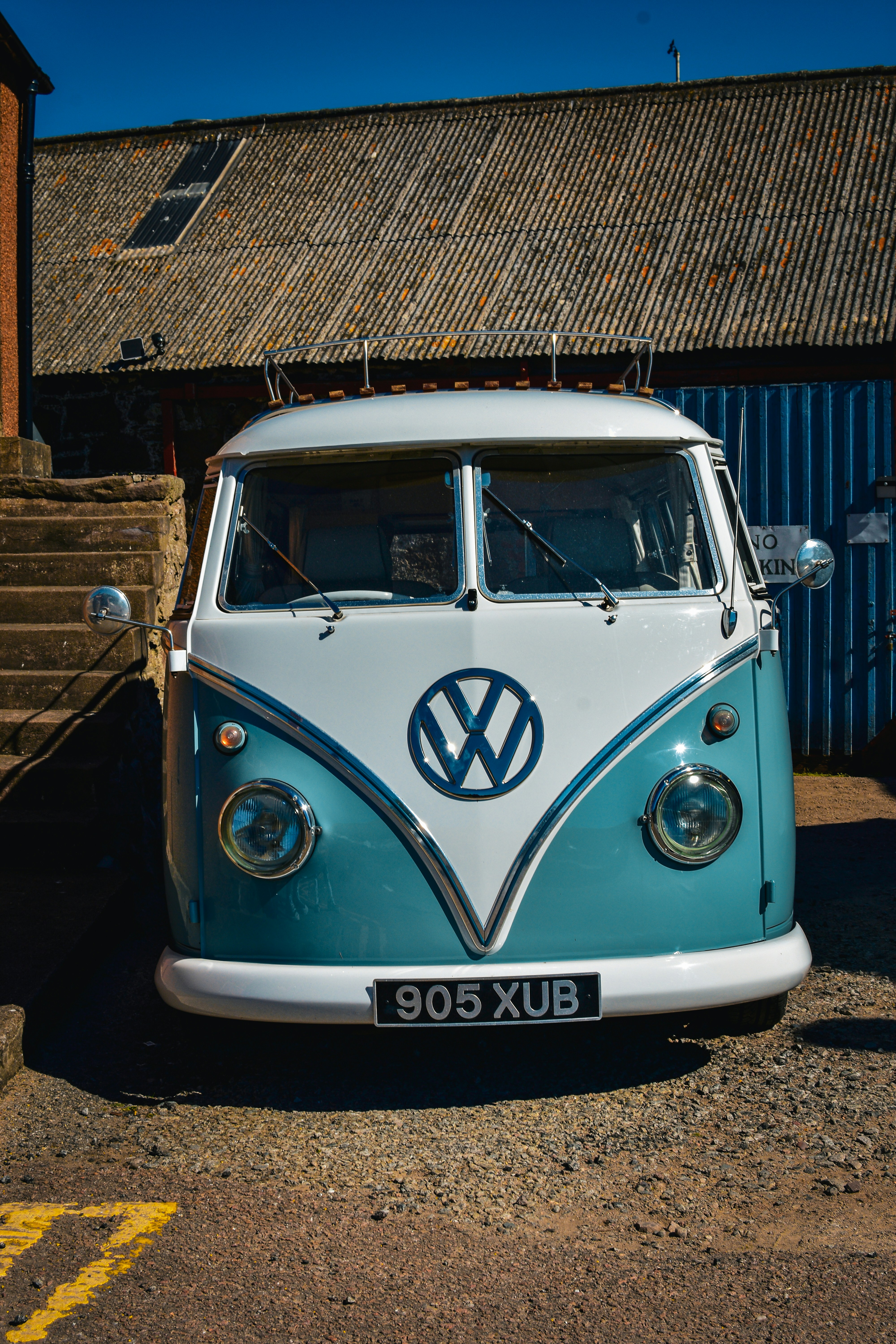 Front view of a vintage Volkswagen van showcasing its iconic design and vibrant colors. The vehicle is parked against a rustic backdrop.
