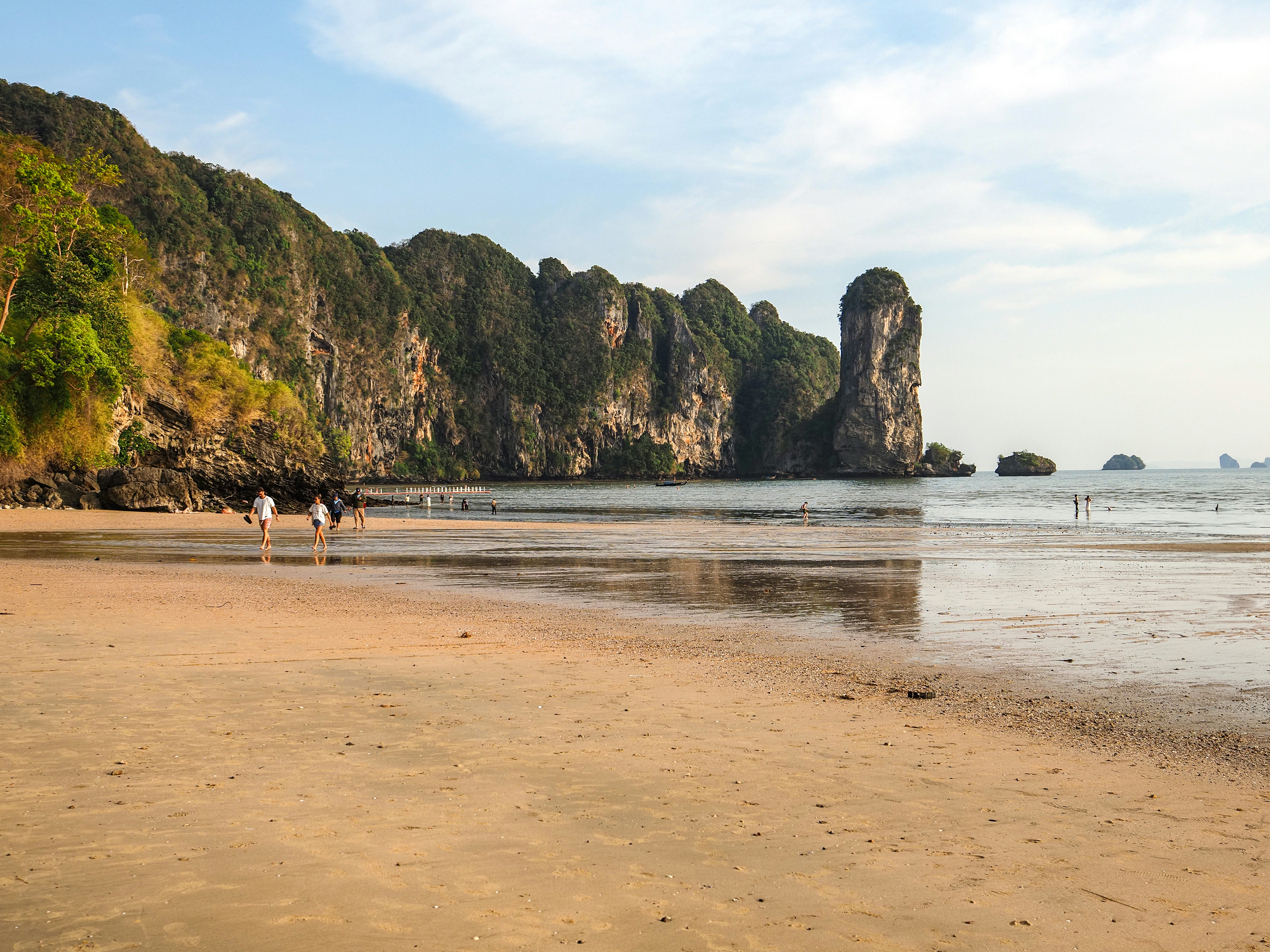 Beachgoers walk along a sandy beach with large cliffs.
