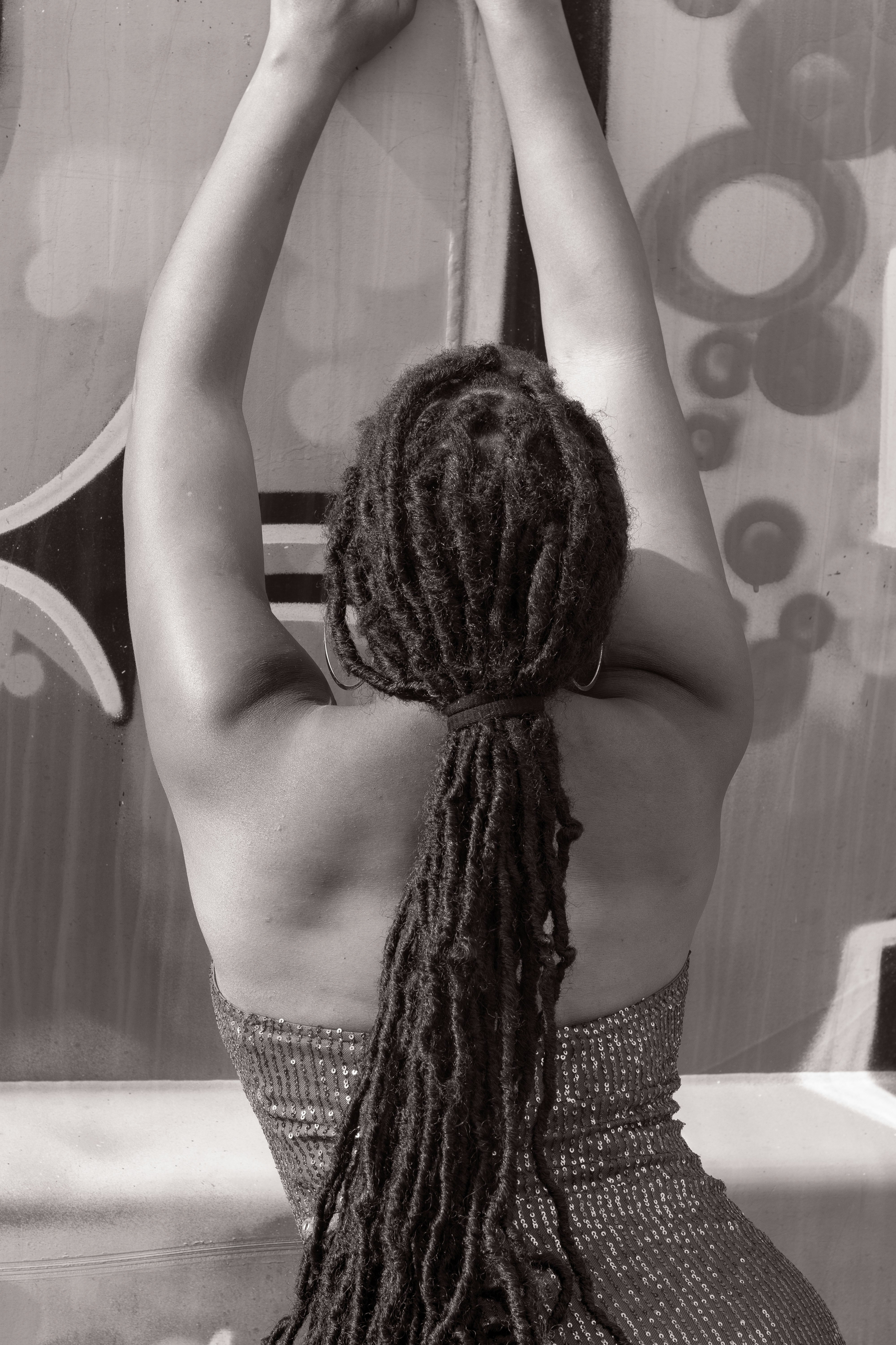 Figure with long dreadlocks reaching towards a colorful mural, showcasing a dynamic interaction with street art.