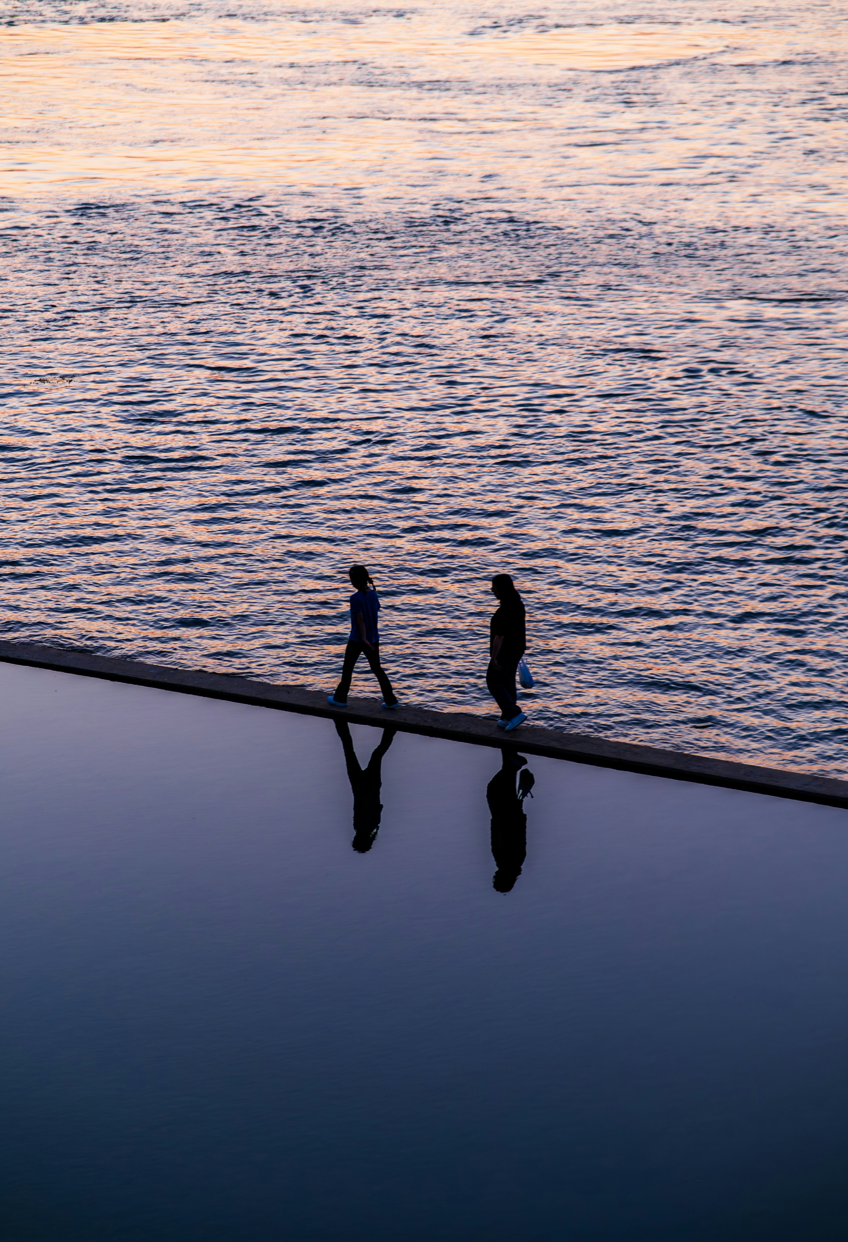 Twilight silhouettes along a narrow pool edge, mirrored in calm water