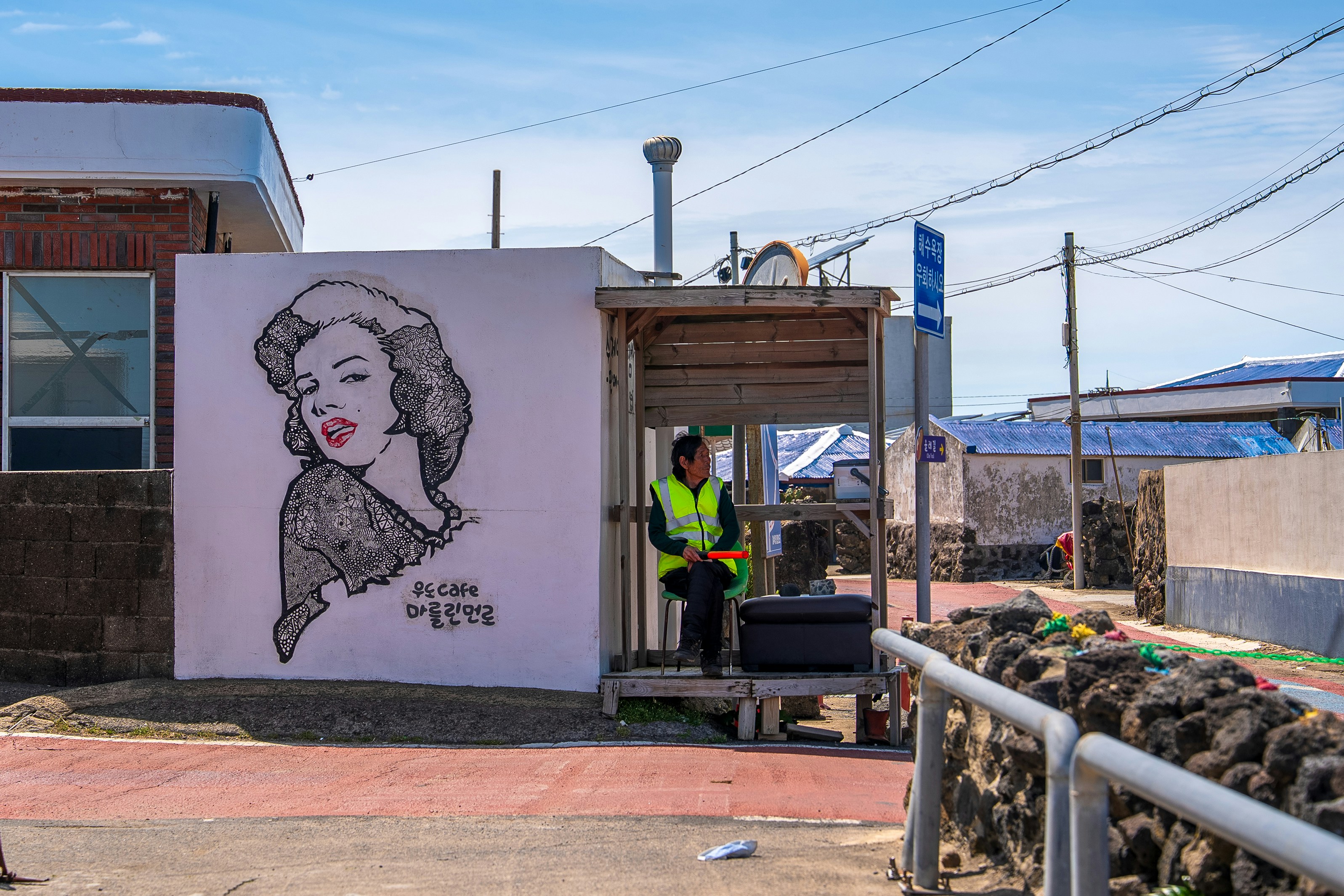 Portrait on a pink wall overlooks a roadside shelter with a worker in a safety vest