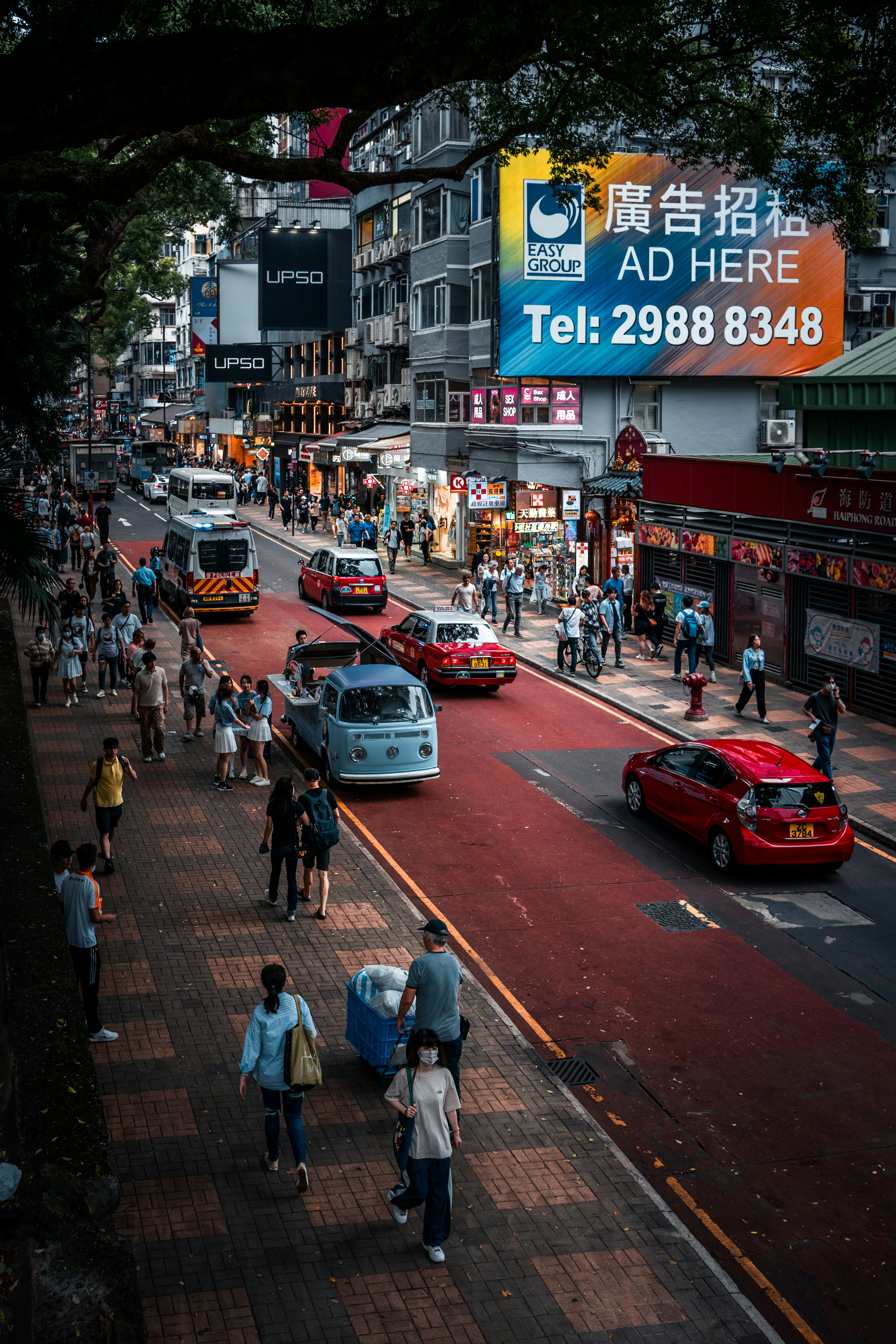 Neon Boulevard: Pedestrians and vintage cars weave through a crowded Hong Kong street at dusk.