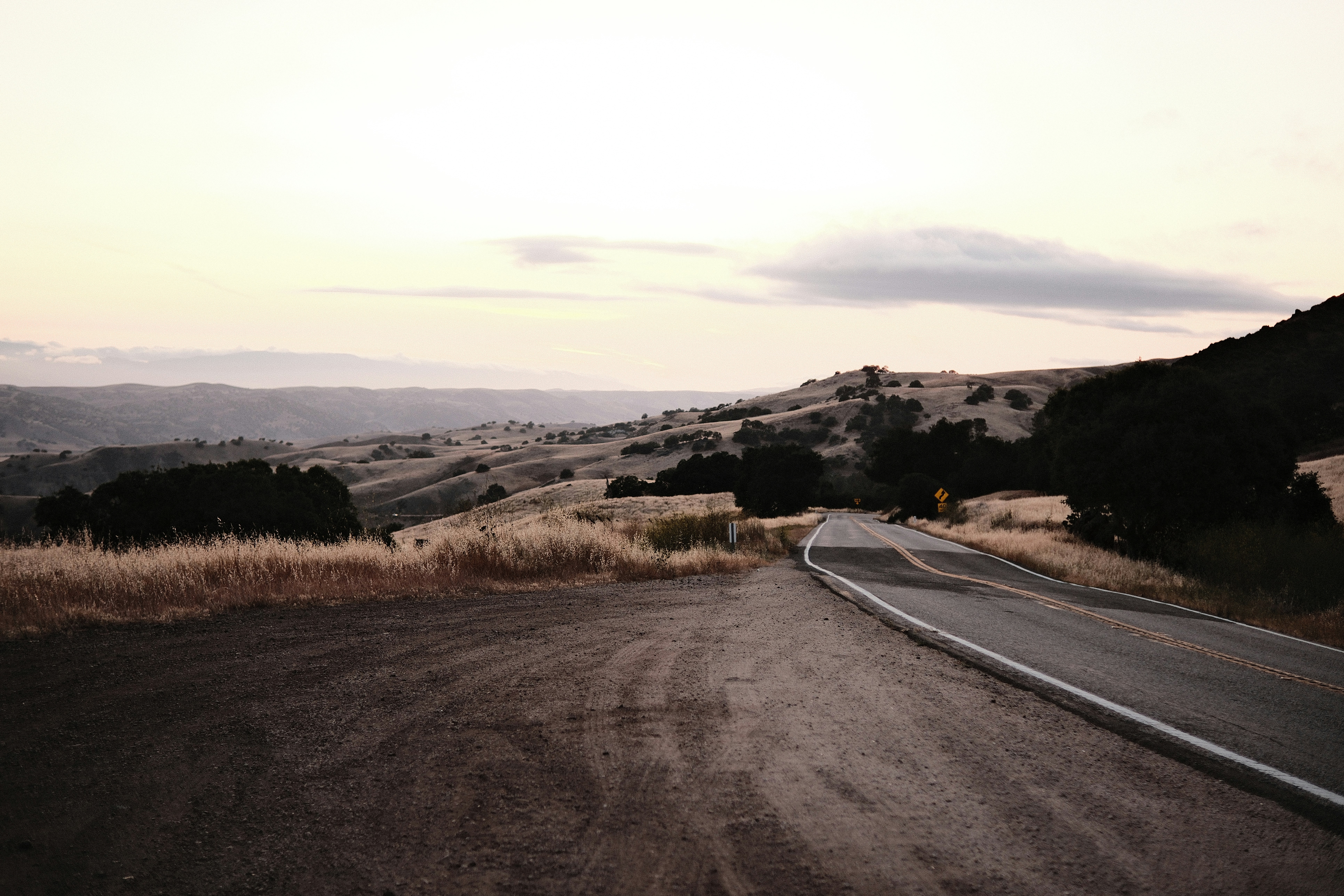 Curving road meanders through golden grasslands and rolling hills under a soft twilight sky.
