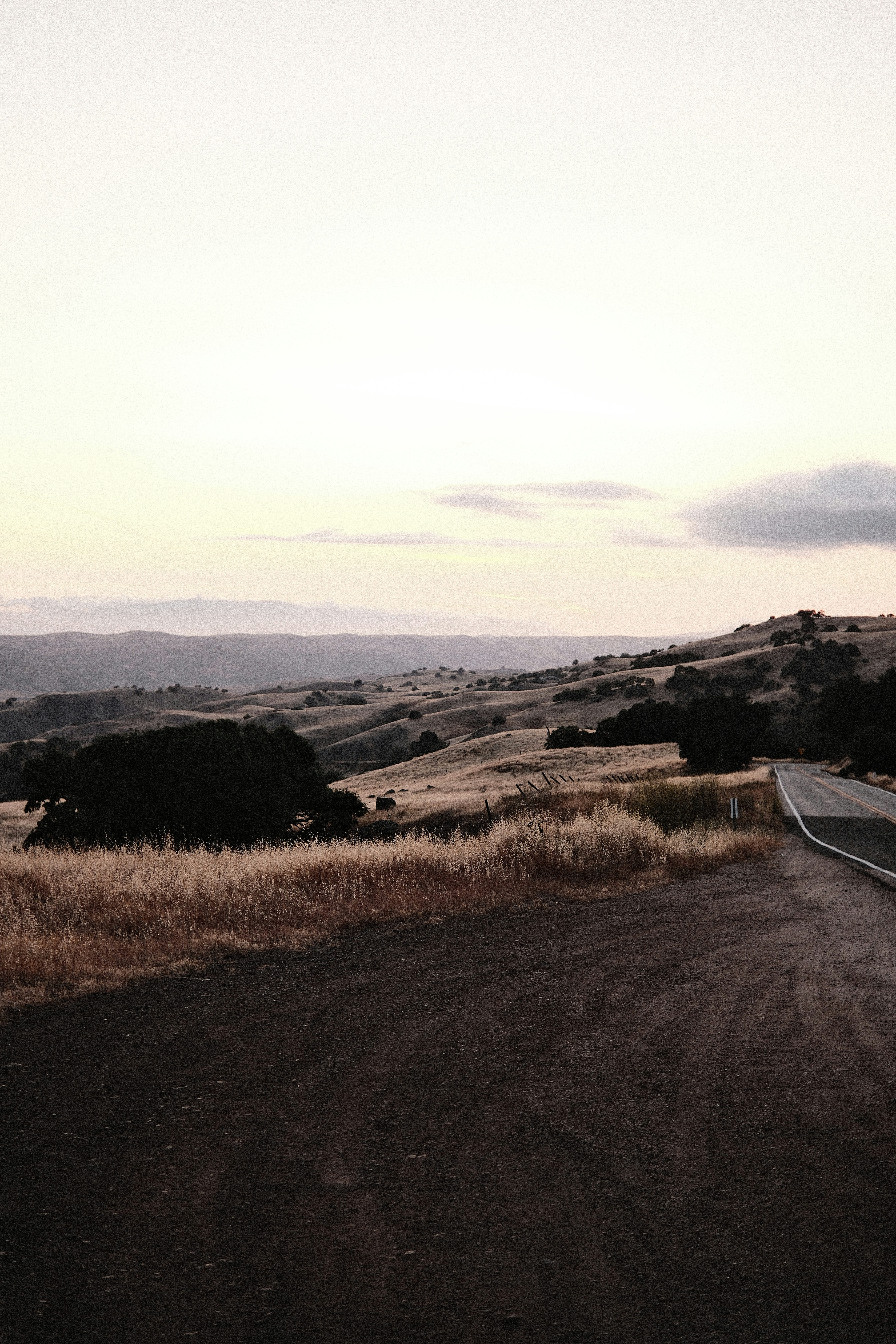 Serene landscape at twilight featuring rolling hills and a winding road, with soft hues in the sky. The scene captures the tranquility of nature transitioning into evening.