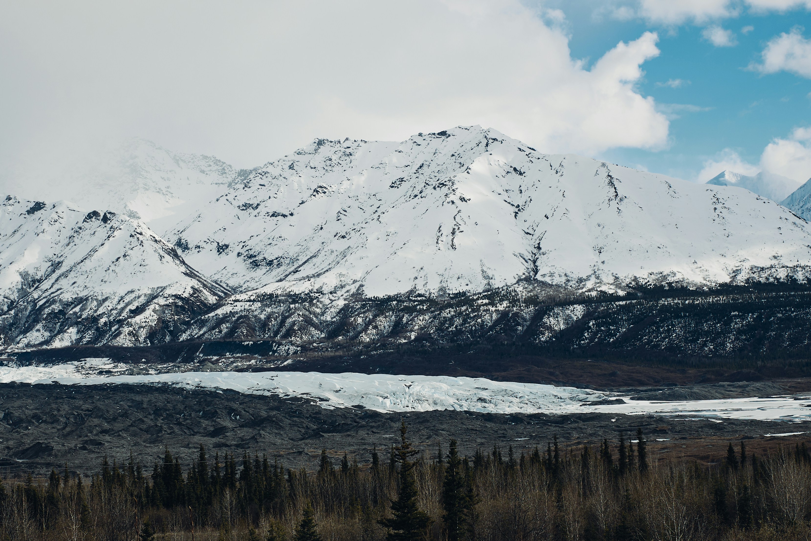 Snow-capped mountains rise majestically above a glacial expanse, framed by a rugged landscape. The scene captures the raw beauty of nature's icy formations.