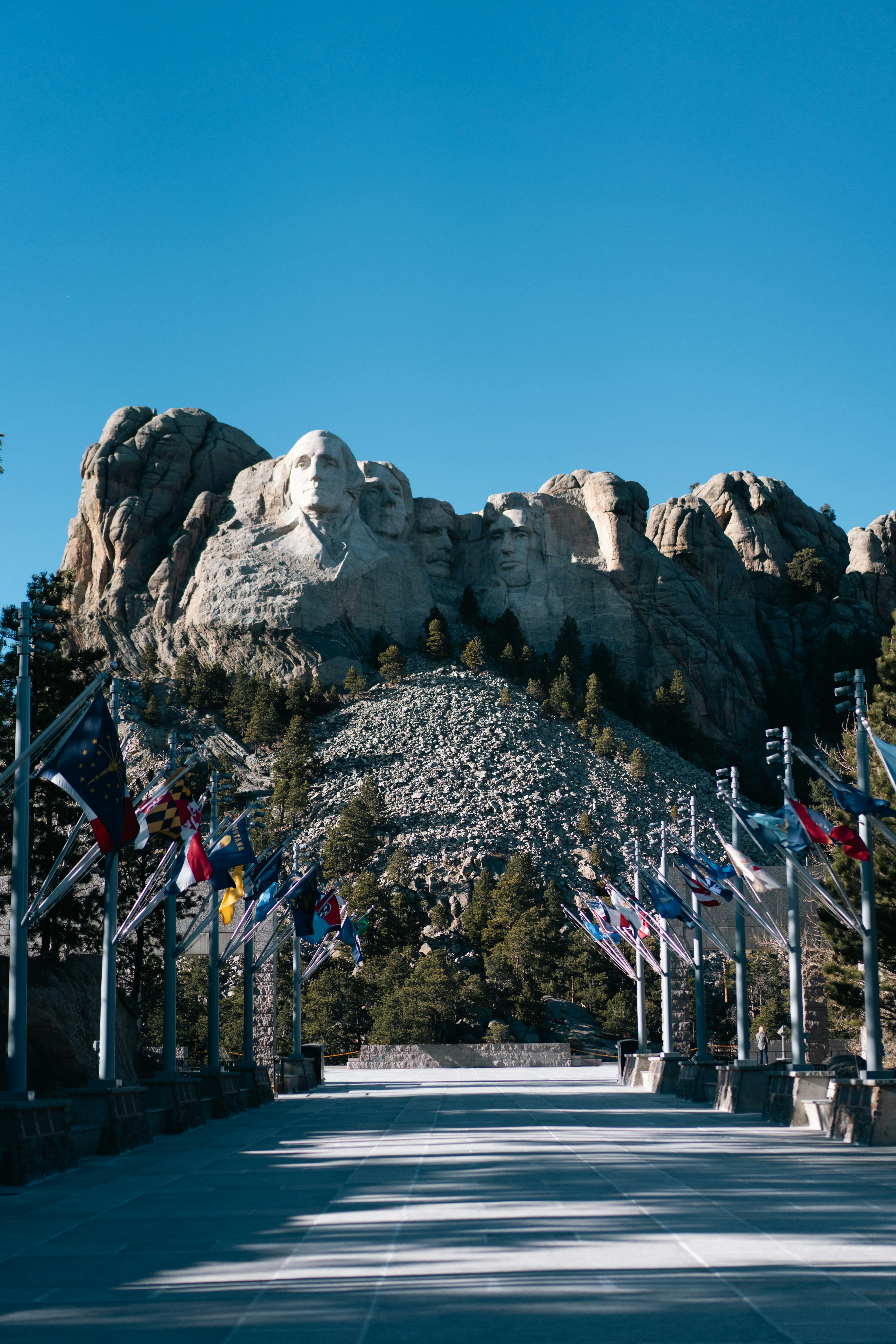 Stone Faces Under Blue Sky: Flags Framing Mount Rushmore Approach