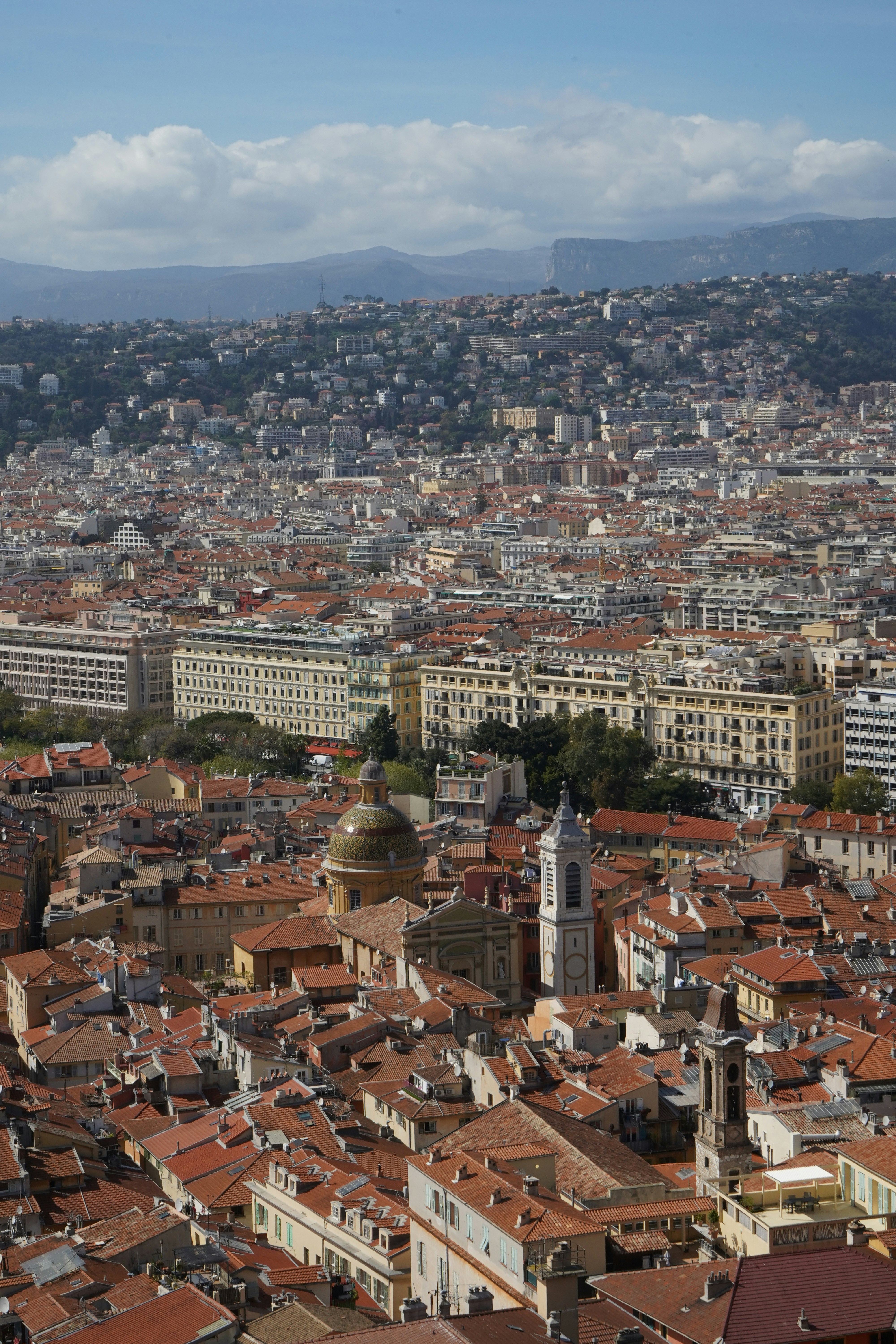Panoramic view of Nice's terracotta rooftops and vibrant architecture, showcasing the city's unique urban landscape against a backdrop of distant hills.