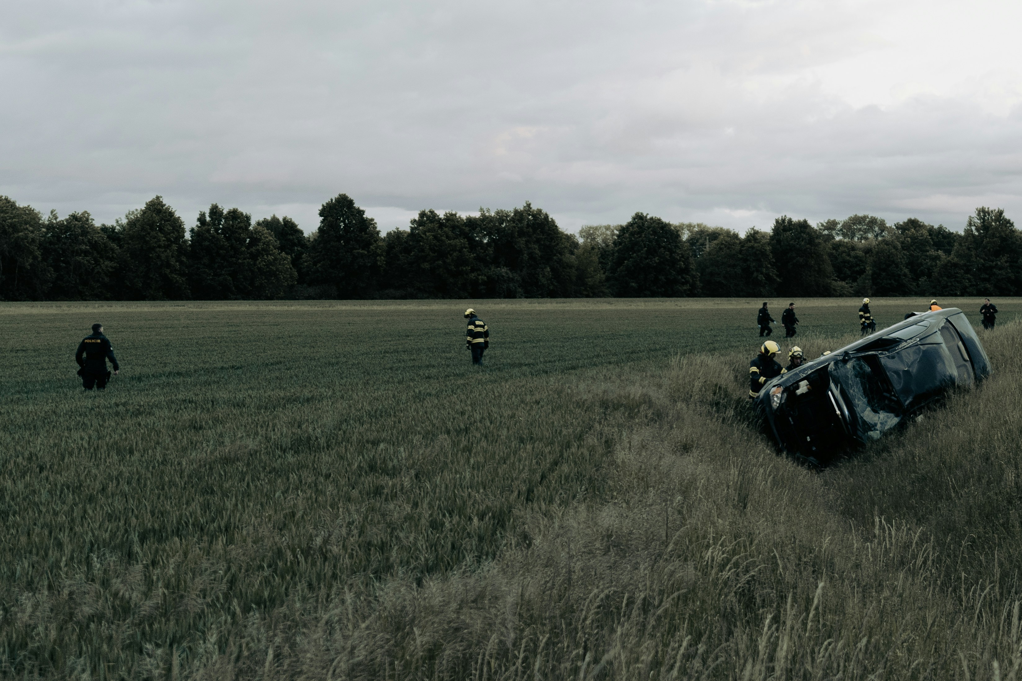 First responders navigate a lush green field towards an overturned vehicle, highlighting the urgency of the situation. The scene captures the intersection of nature and emergency response efforts.