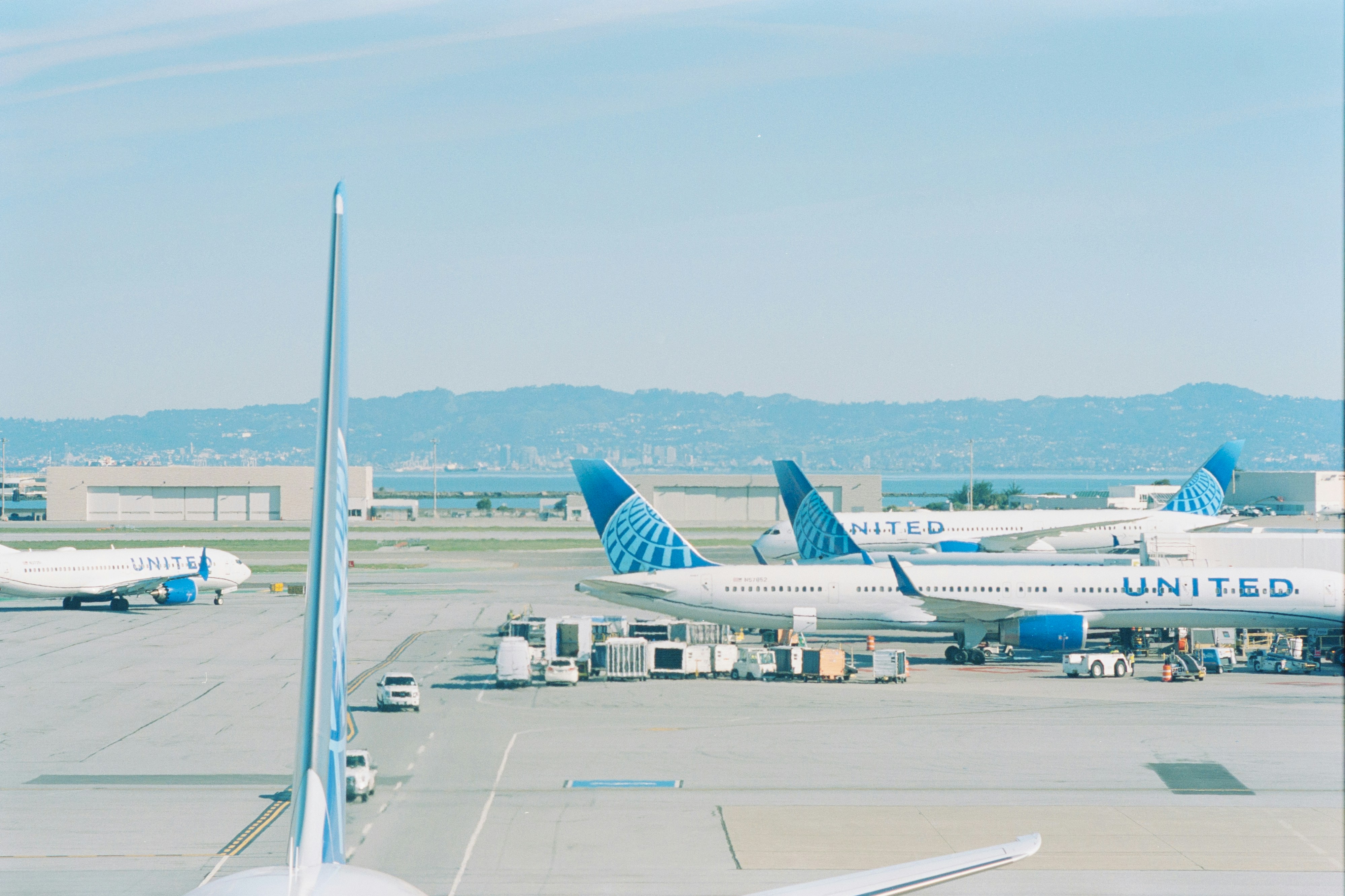 United Airlines jets parked on the tarmac with mountains in the background, showcasing a clear day at the airport.