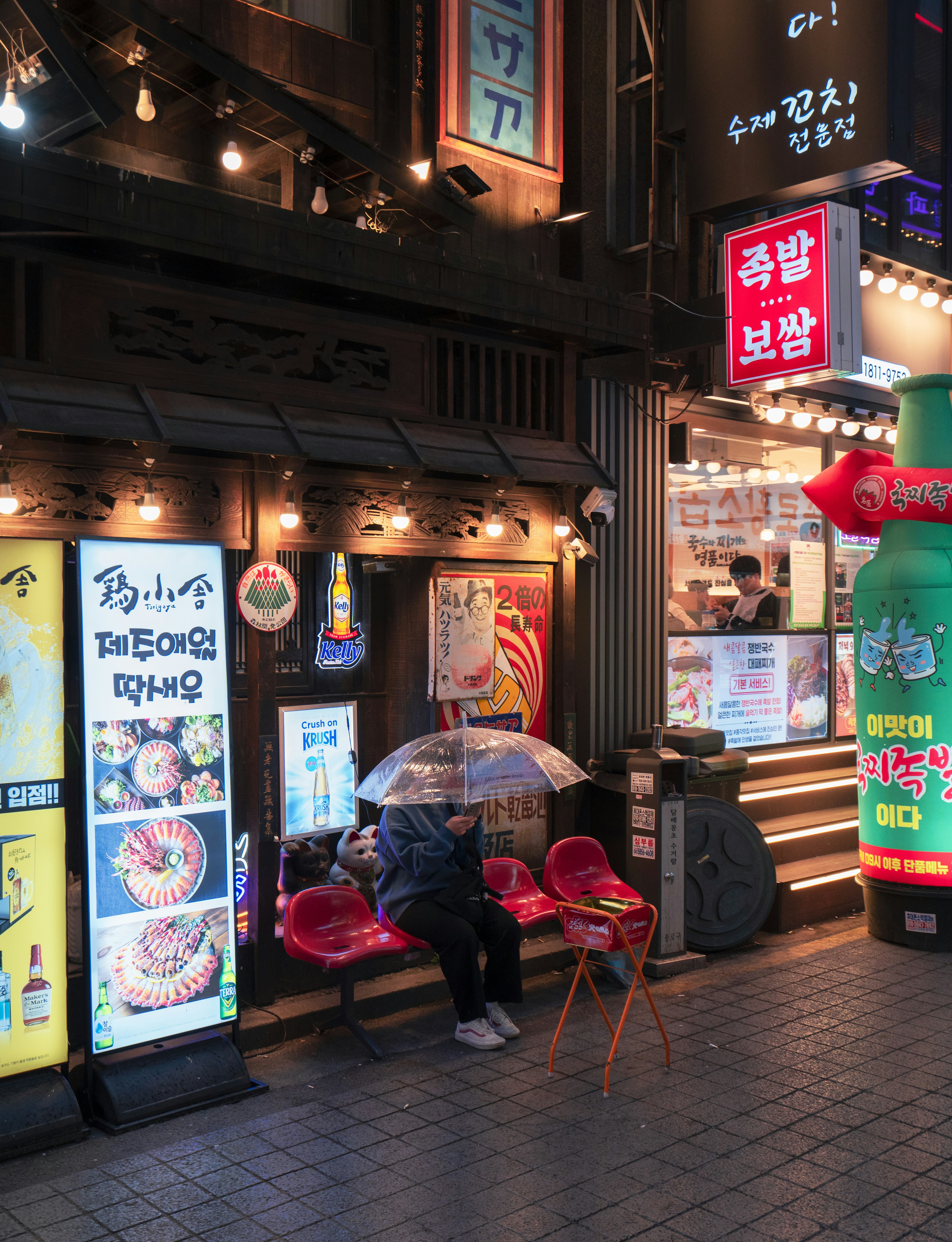 A person sits under umbrella outside a korean restaurant.
