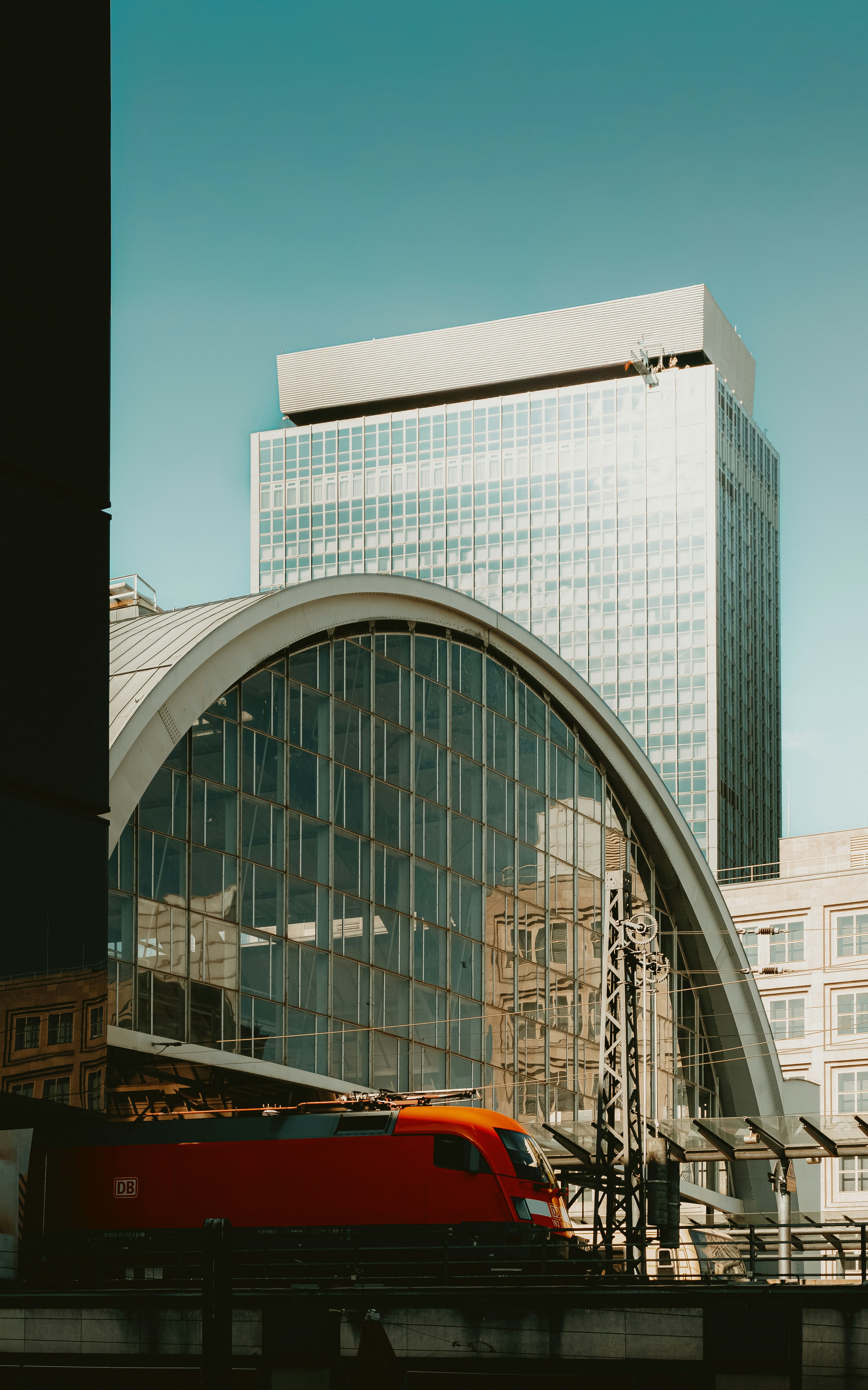 Red Locomotive Under a Glass Arch: Transit Through a Glass-Fronted Skyline