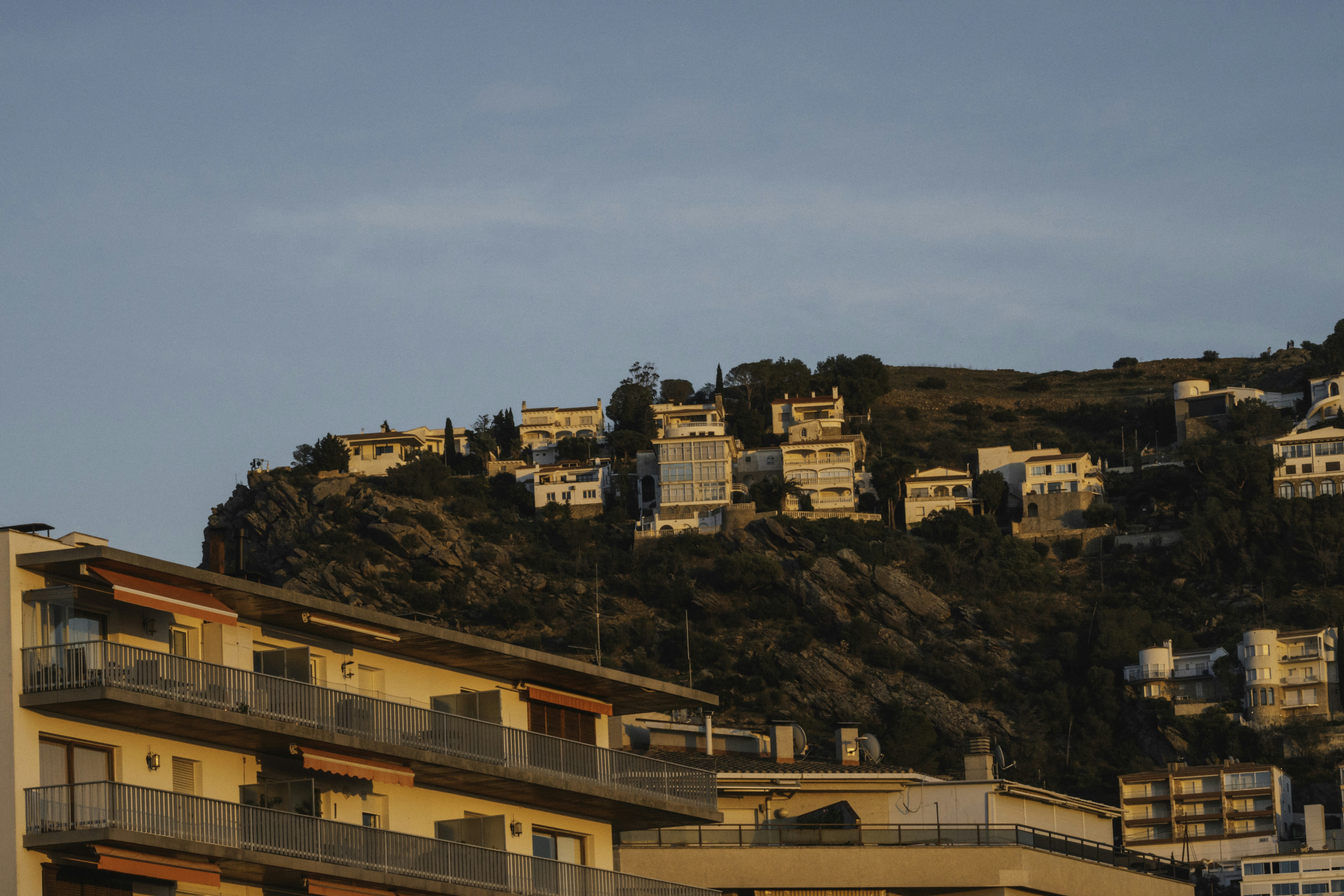 Modern buildings perched on a hillside, blending seamlessly with the rocky terrain and evening sky.