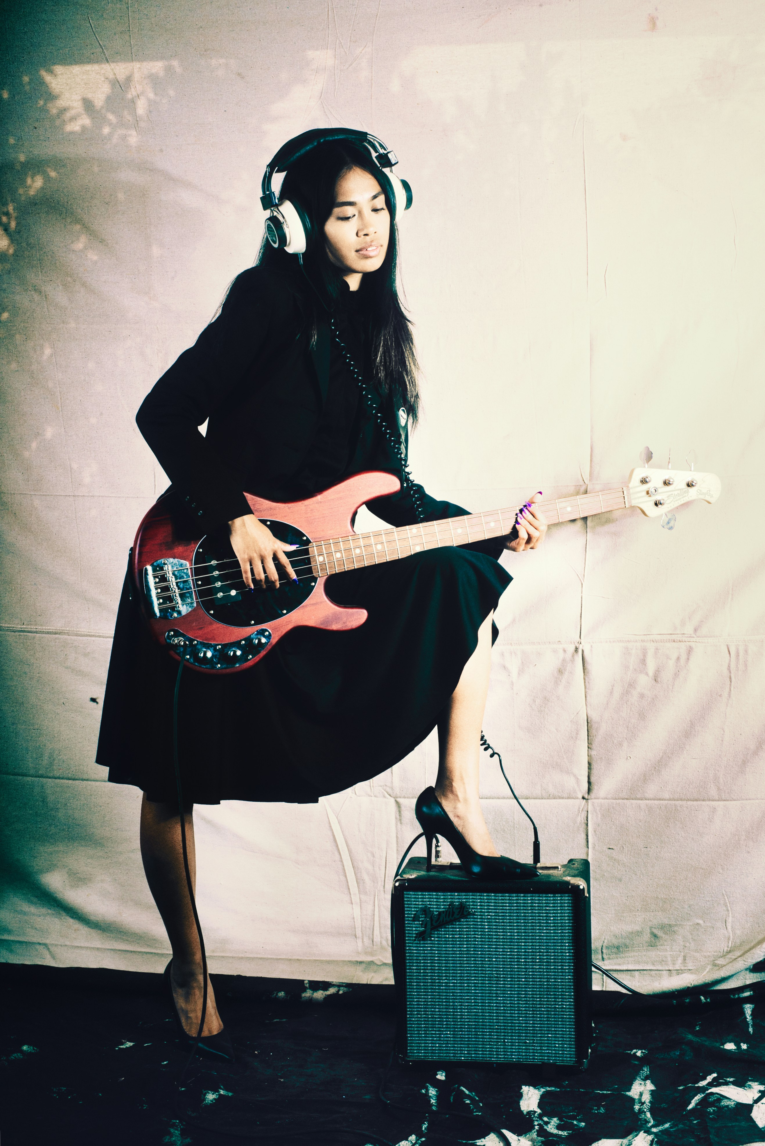 @izzieoooo | A woman plays bass guitar, listening with headphones.
