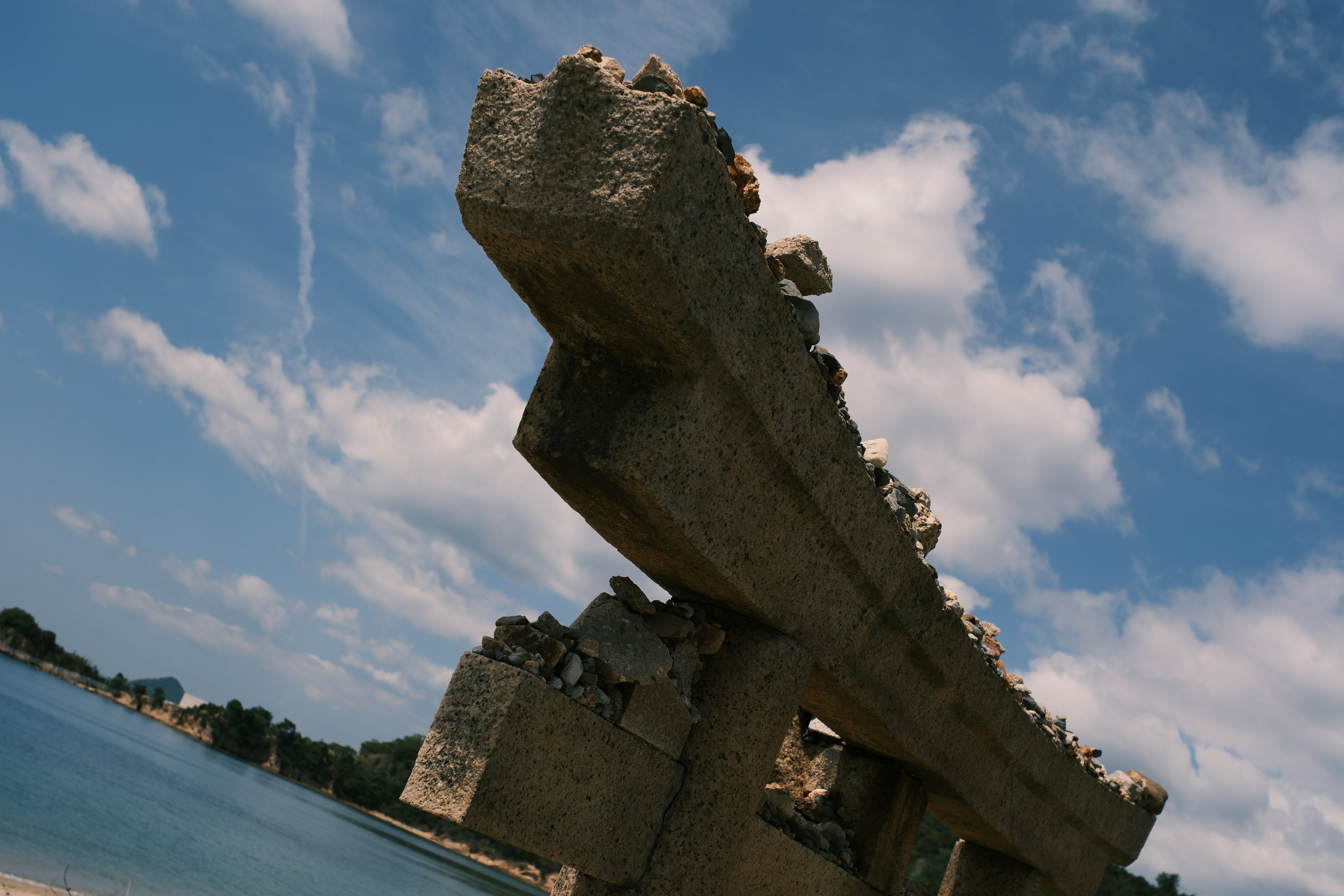 Tilted Sentinel Over Quiet Water: A Weathered Stone Remnant Reaches Toward the Sky